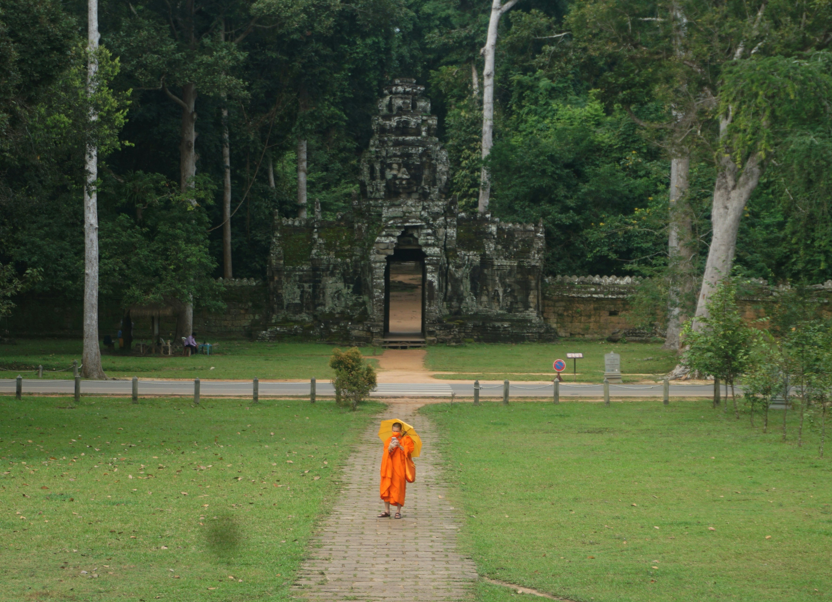 Monk in vibrant orange robe walking along a stone path leading to an ancient temple surrounded by lush greenery.