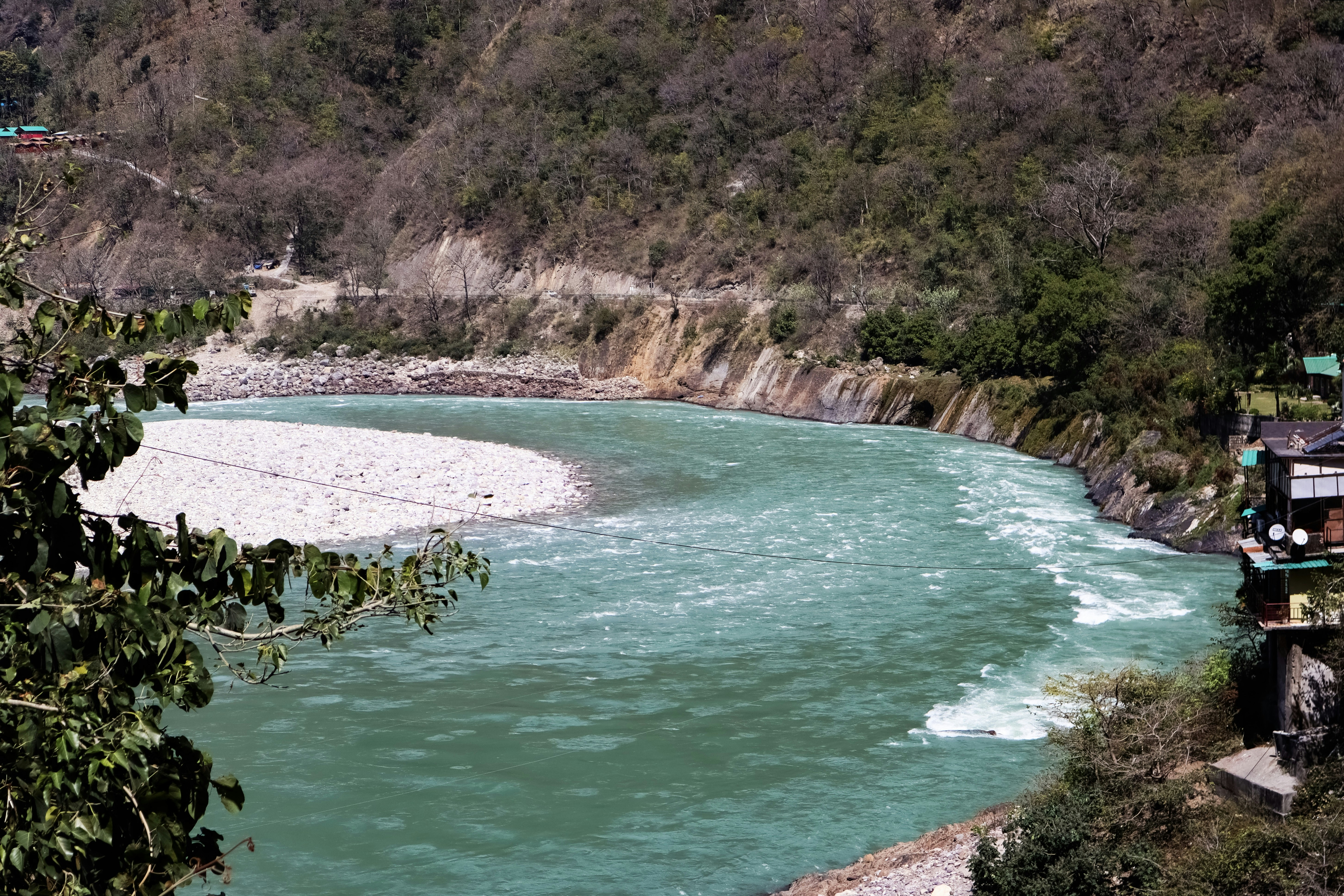 Confluence of two rivers forming turquoise waters surrounded by lush hills and rocky banks.