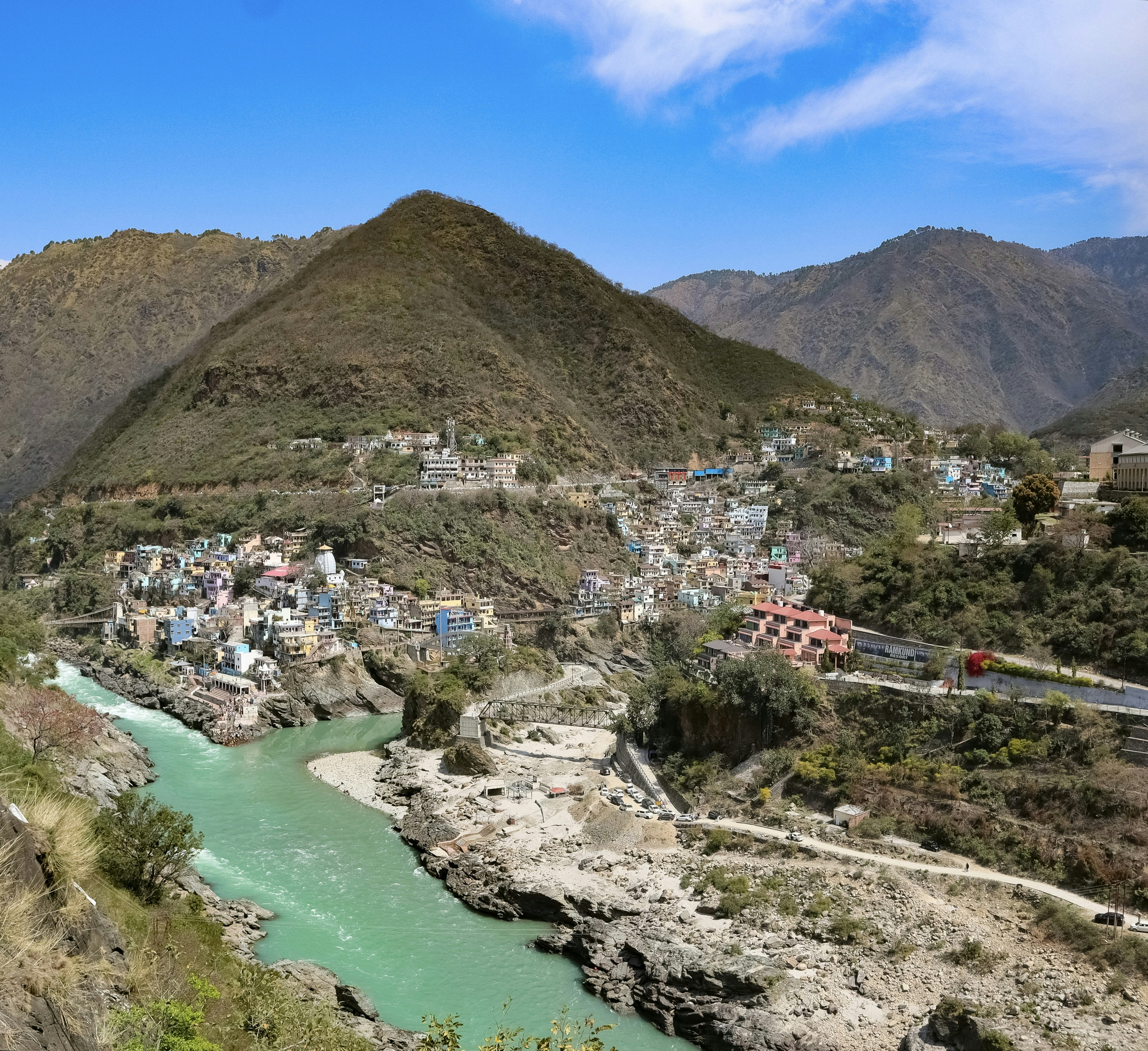 A vibrant riverside village nestled between lush mountains, showcasing colorful homes and winding roads alongside a flowing river.
