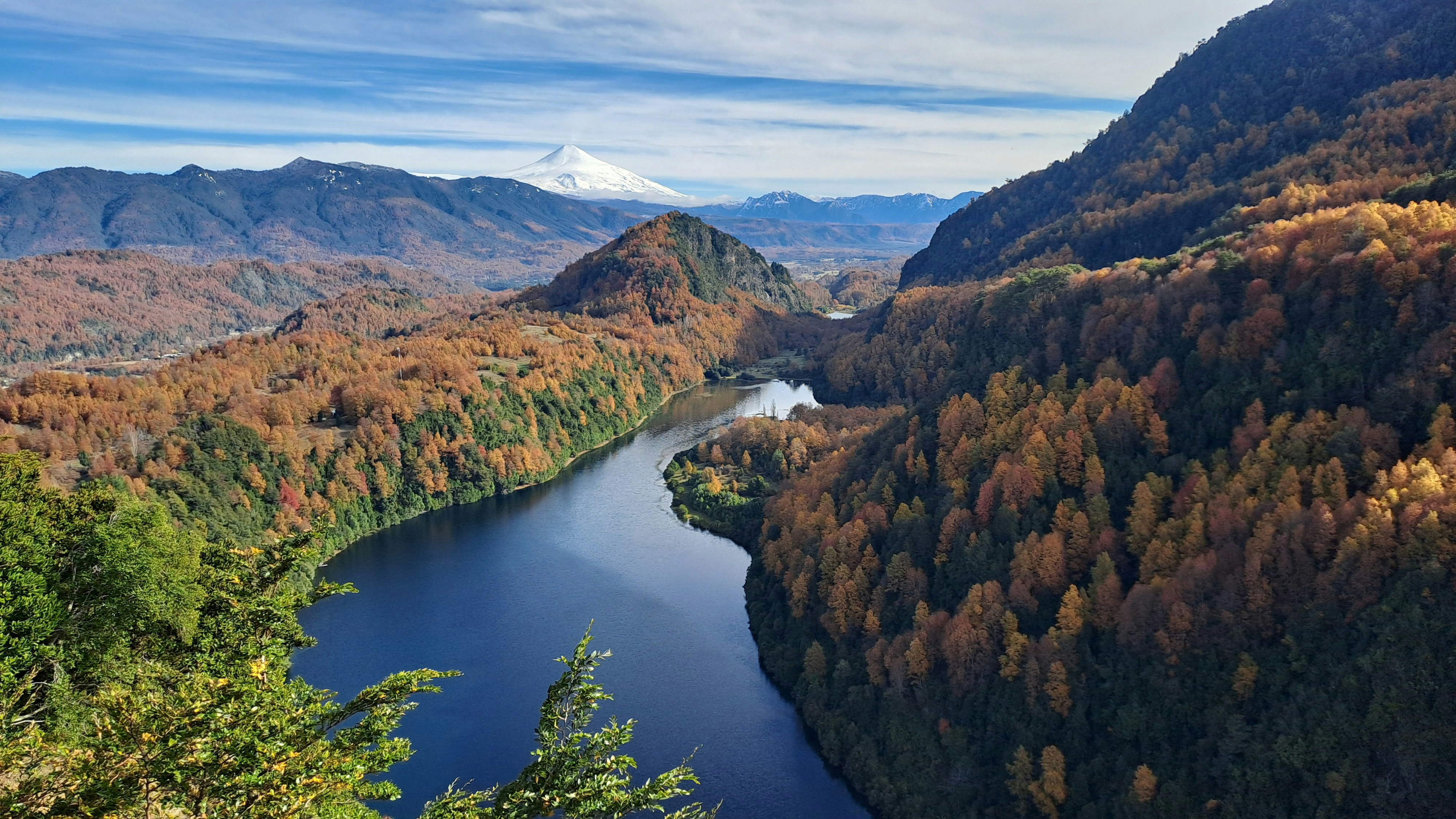 River winding through forested mountains with autumn foliage under a clear sky.