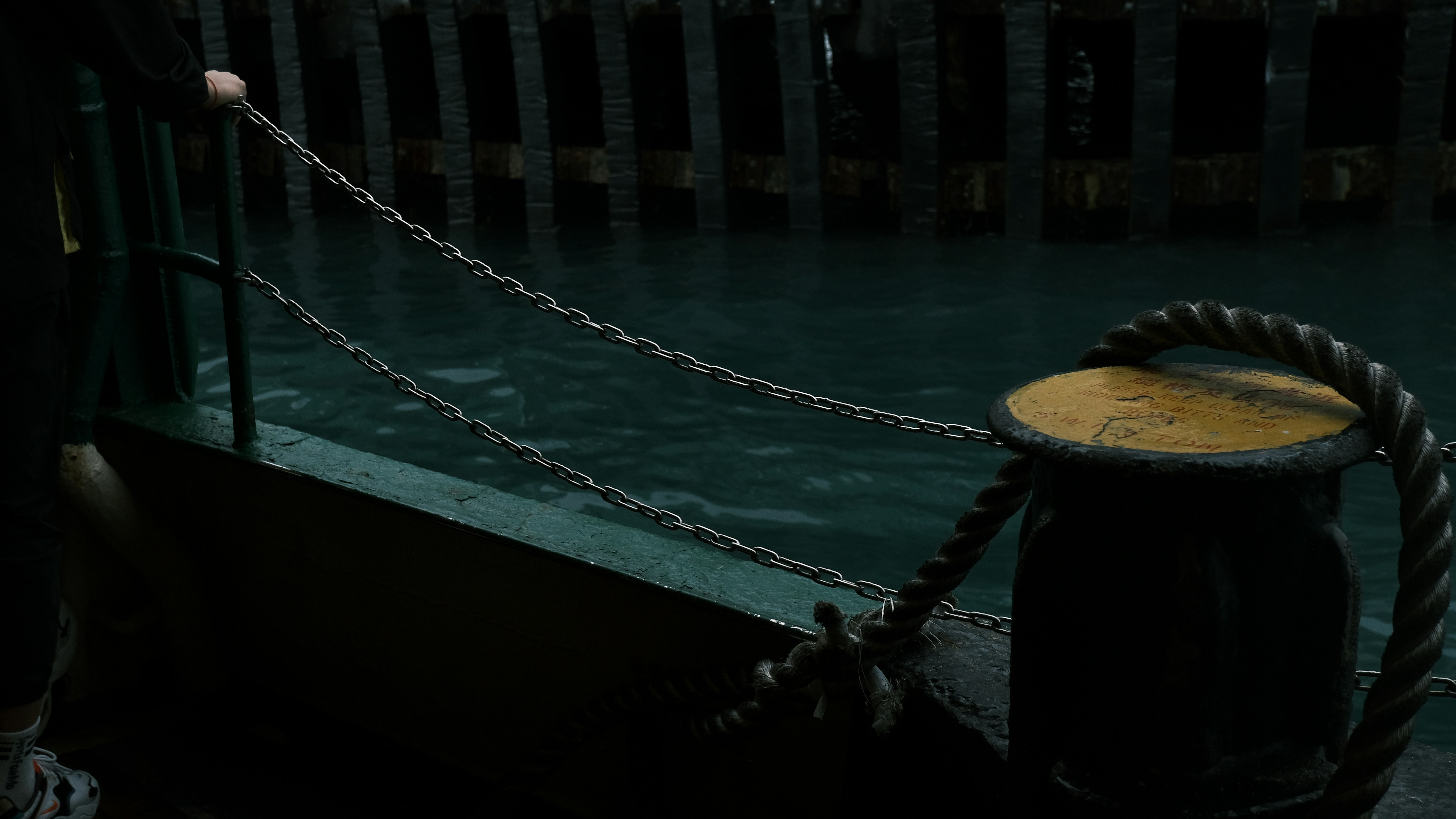 Rope tied to a bollard on a boat against a darkened waterfront.