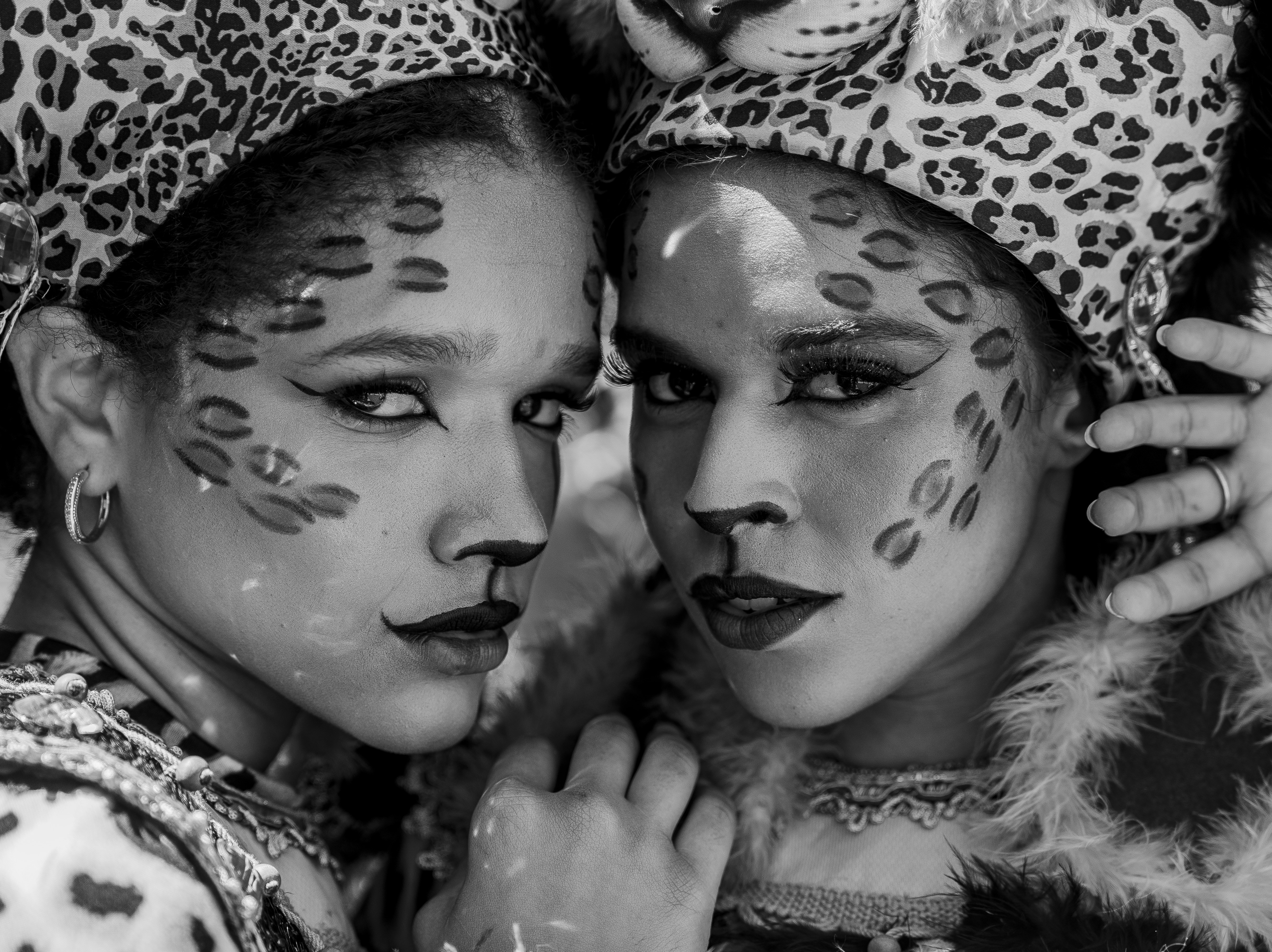 Two individuals in leopard costumes with painted faces, embracing in a black and white portrait.