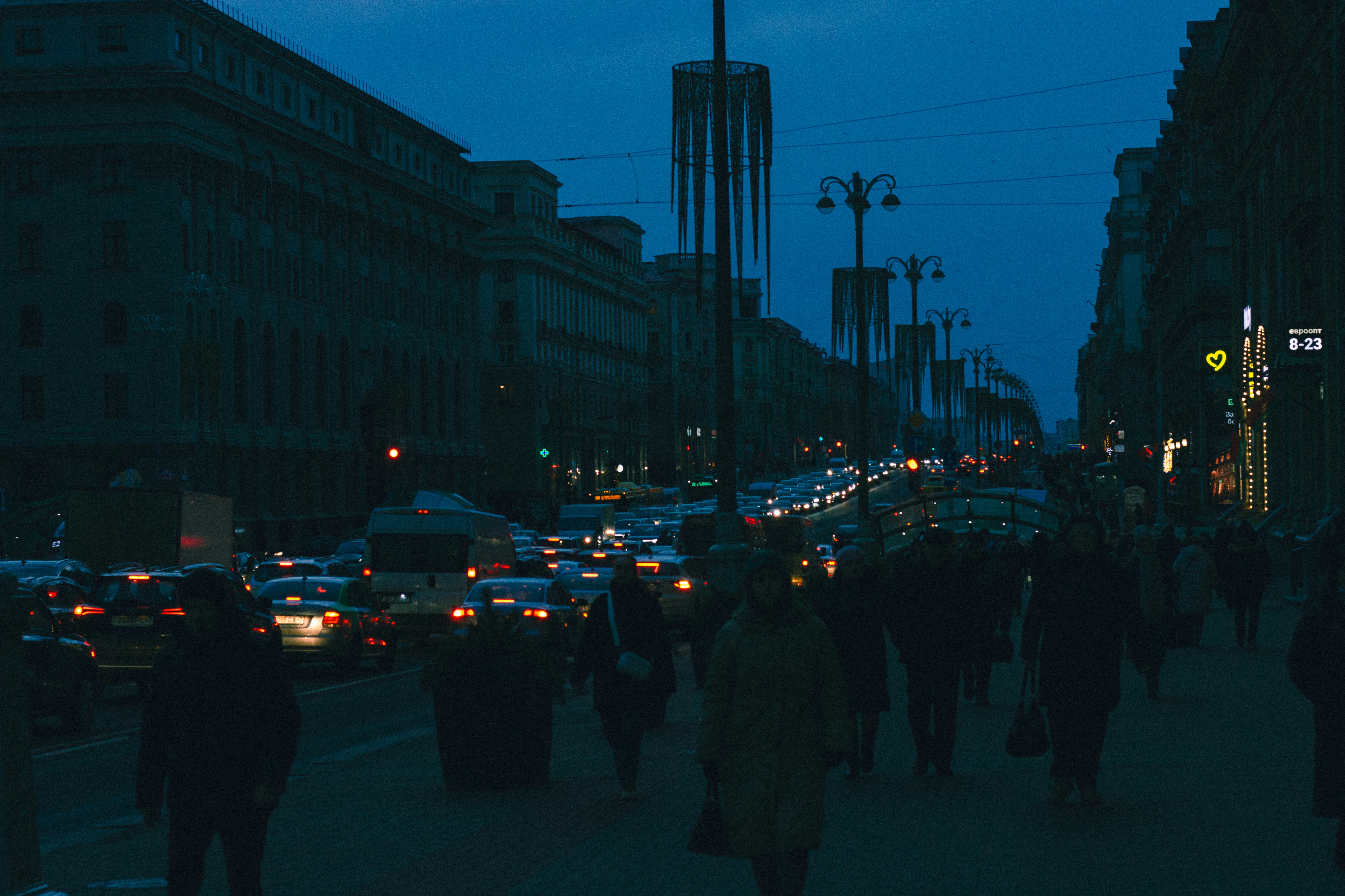 City street bustling with cars and pedestrians under a twilight sky.