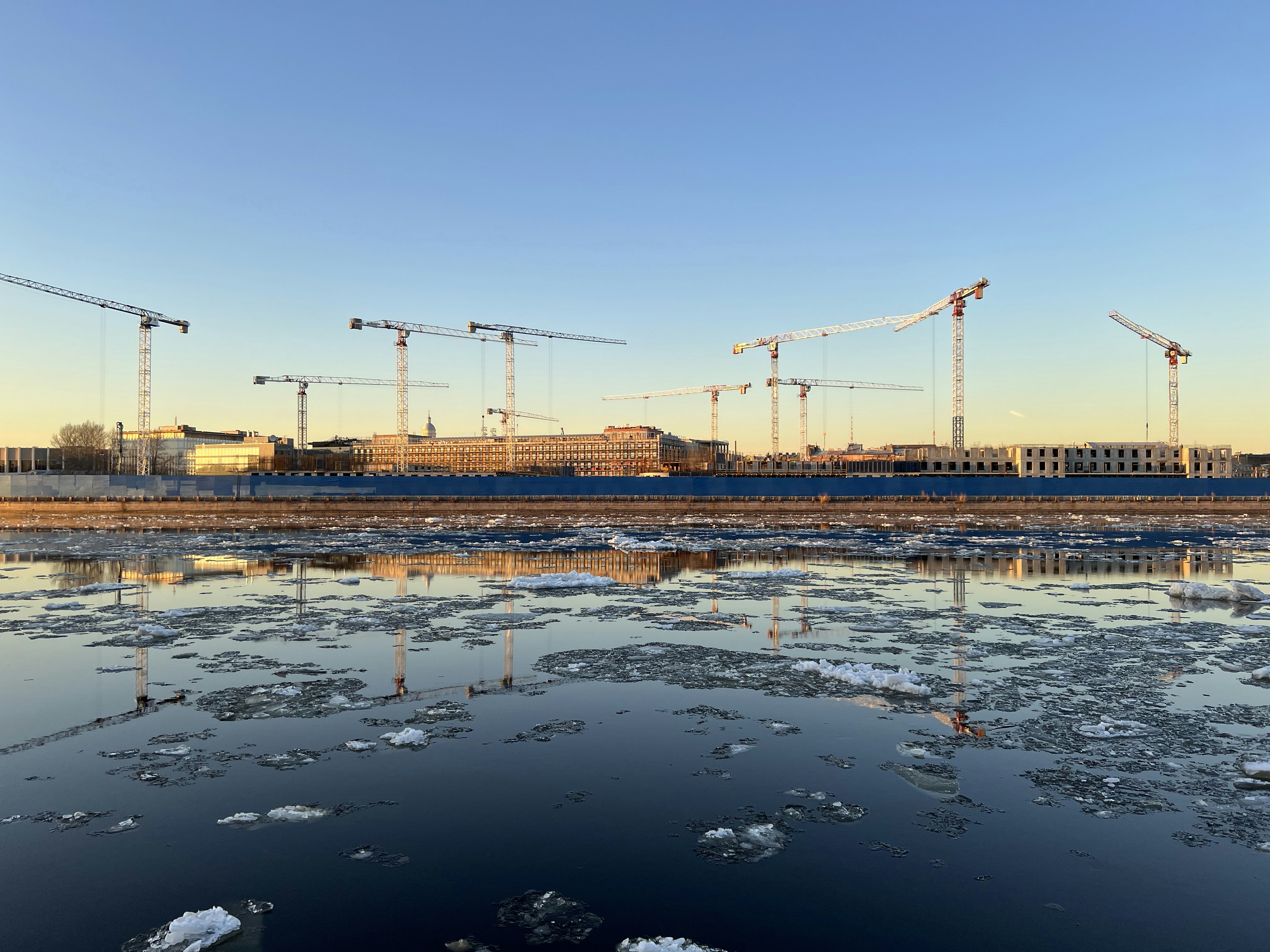 Construction cranes reflected in icy water.