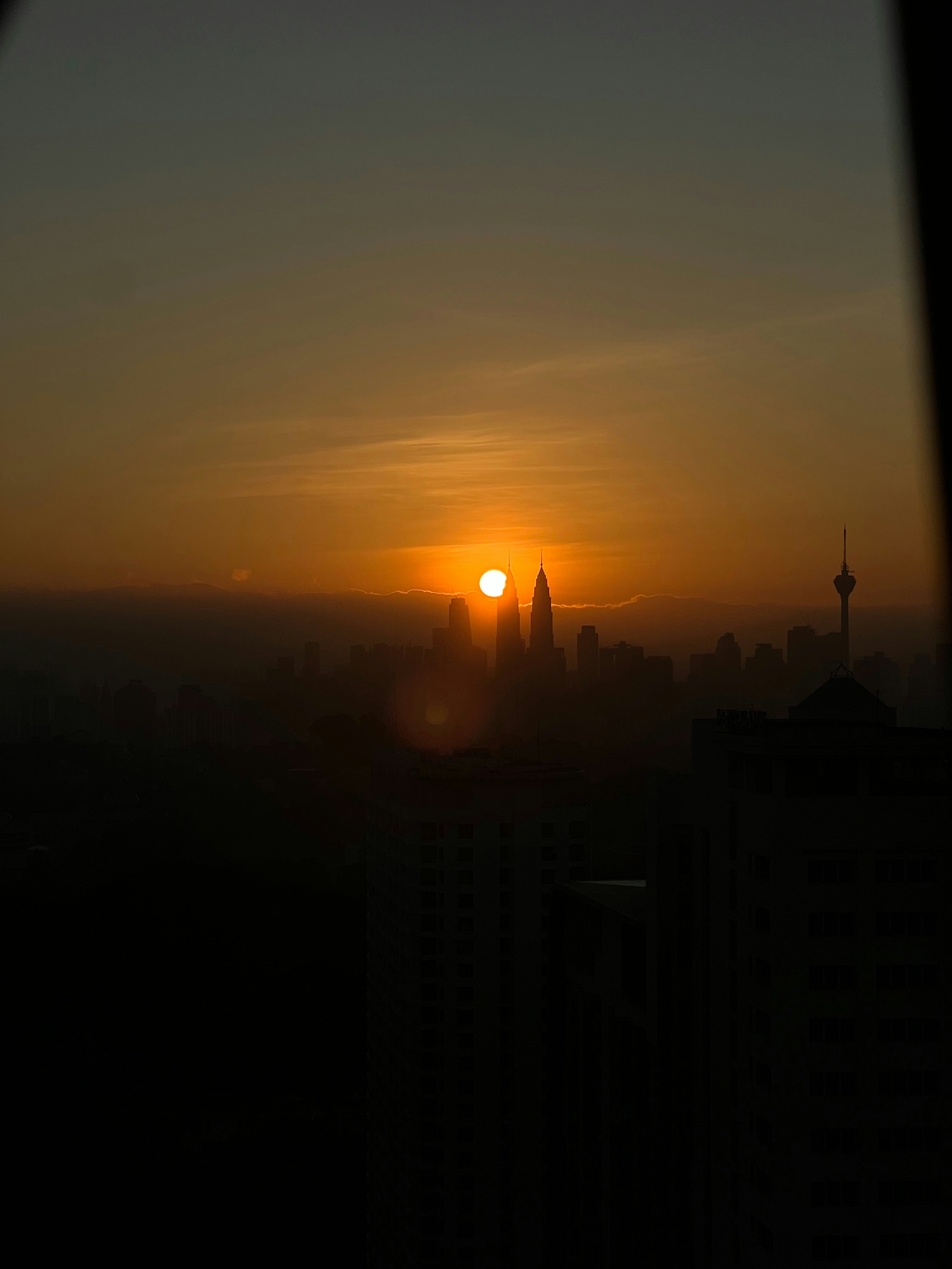 Sunrise casting a warm glow over a city skyline with silhouetted skyscrapers.