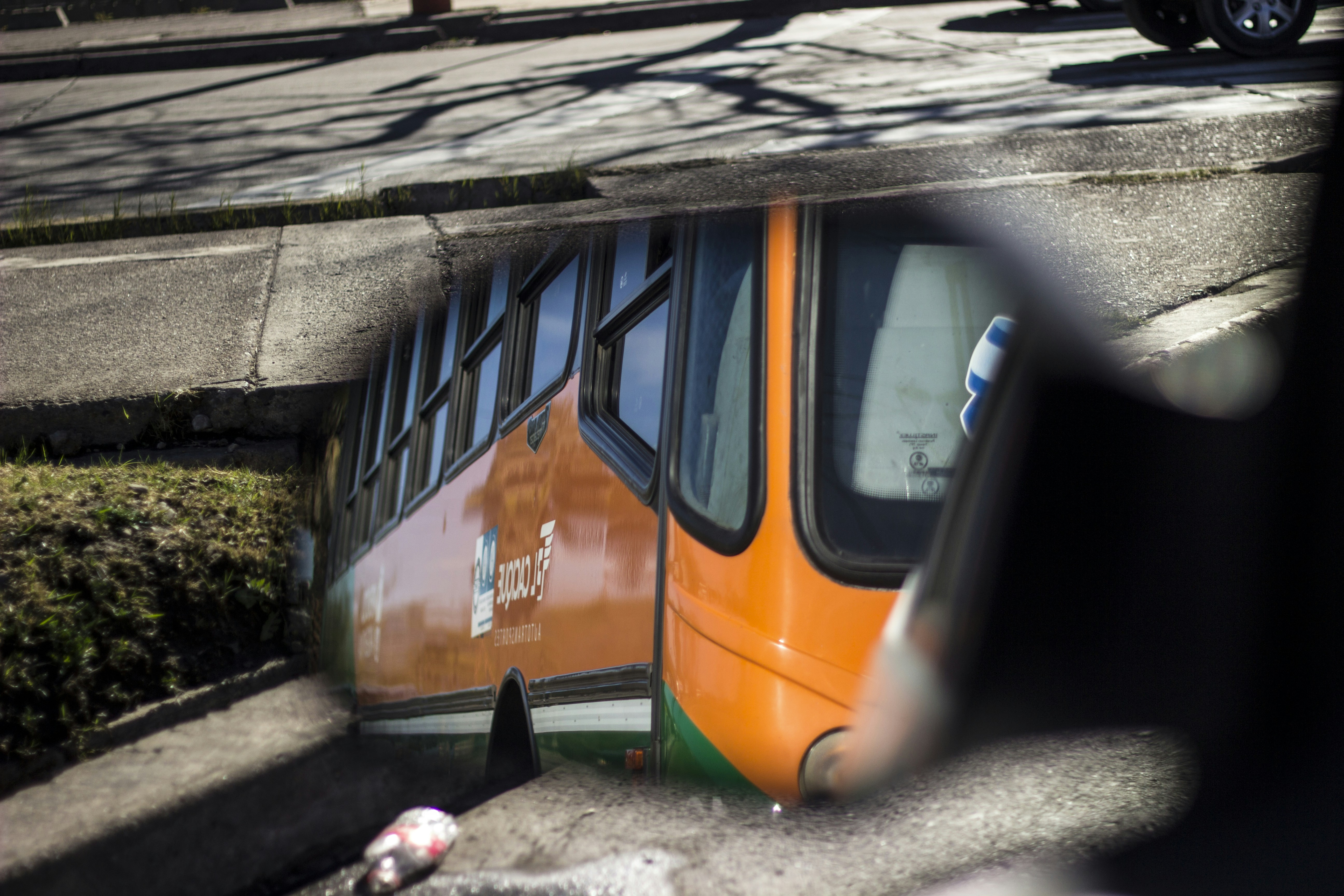 Orange bus reflected in a side mirror, surrounded by urban street textures.
