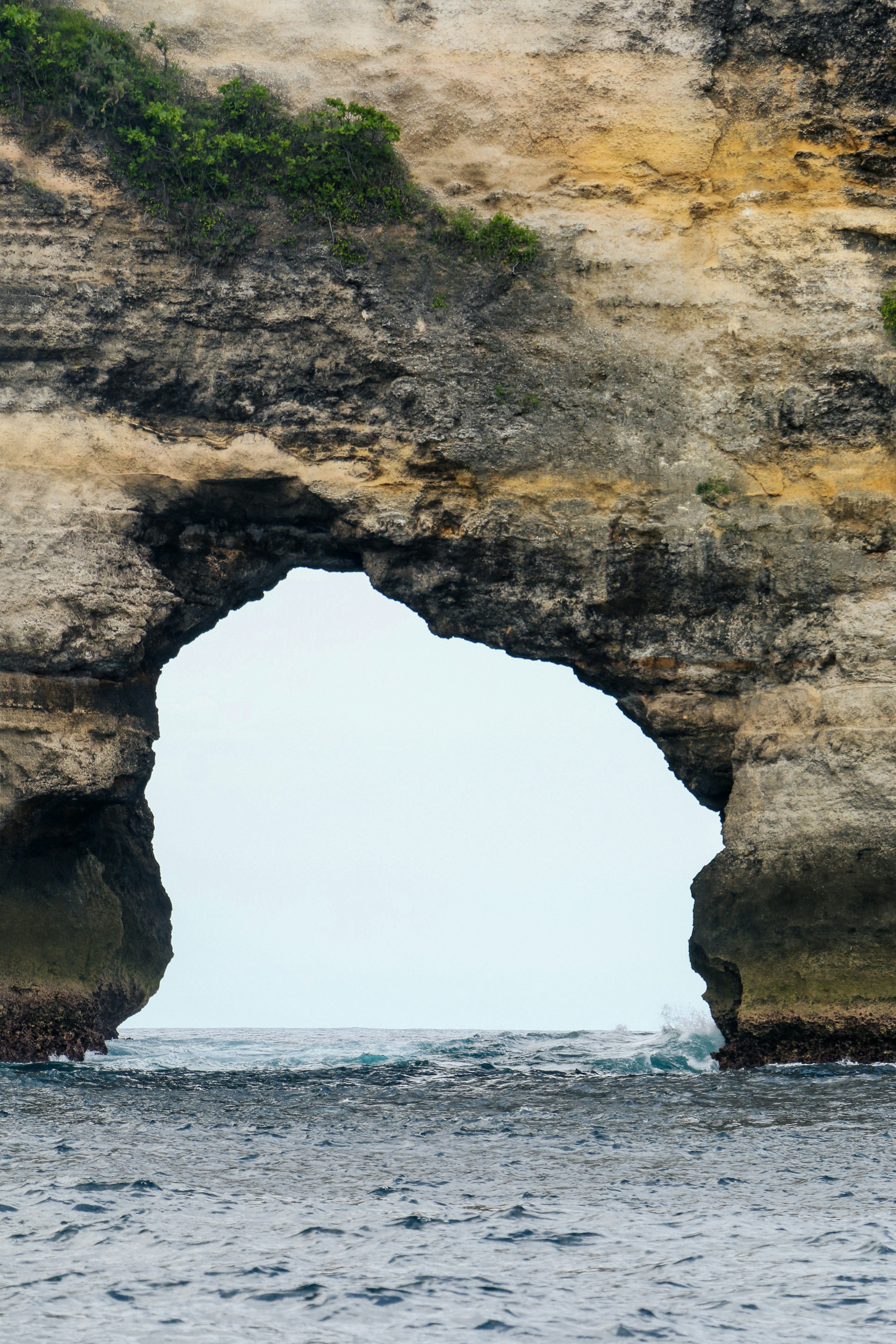 Rock formation with a large arch over the ocean, topped with green vegetation.