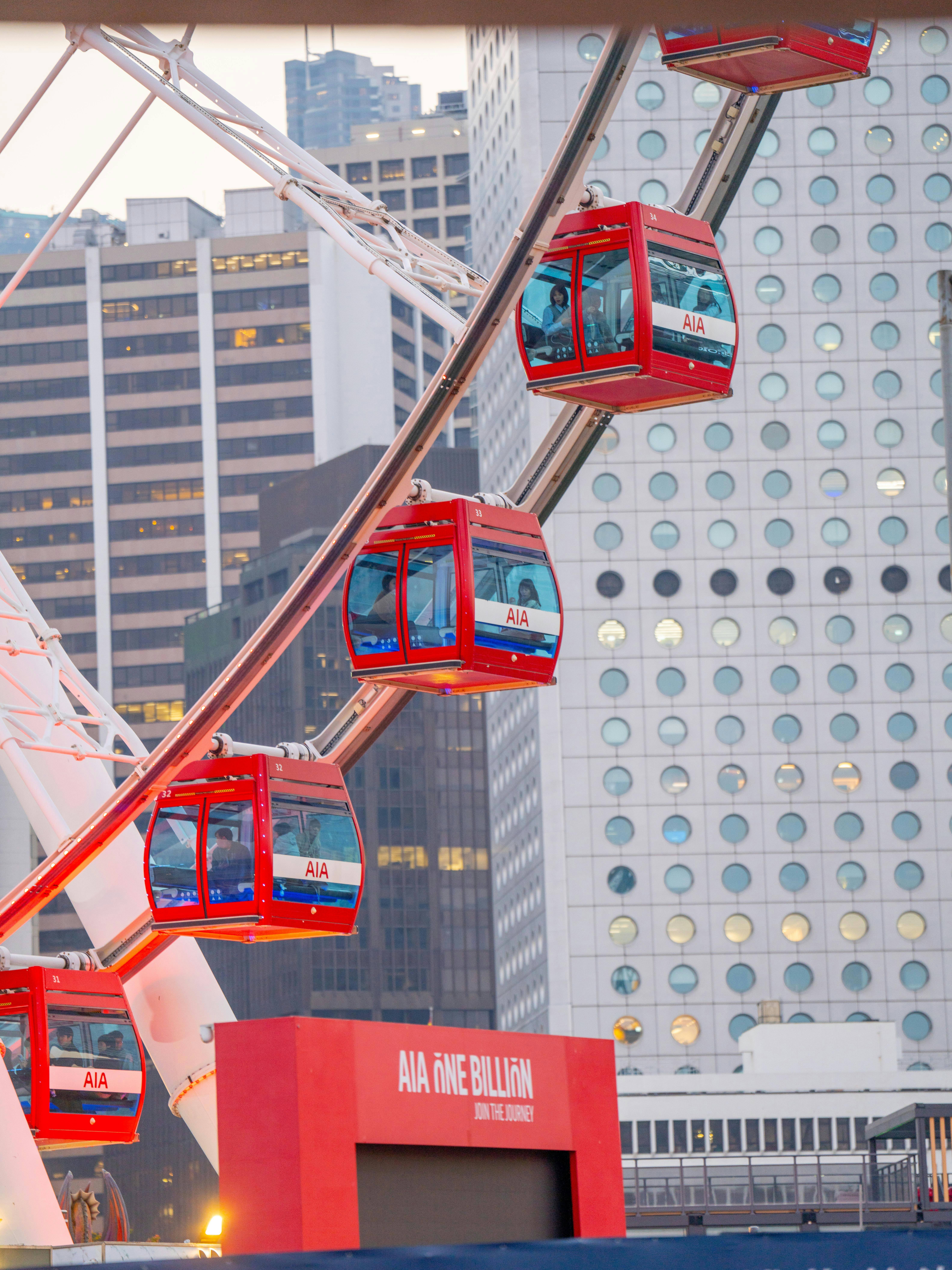 A ferris wheel with red cabins in front of buildings. photo – Free ...