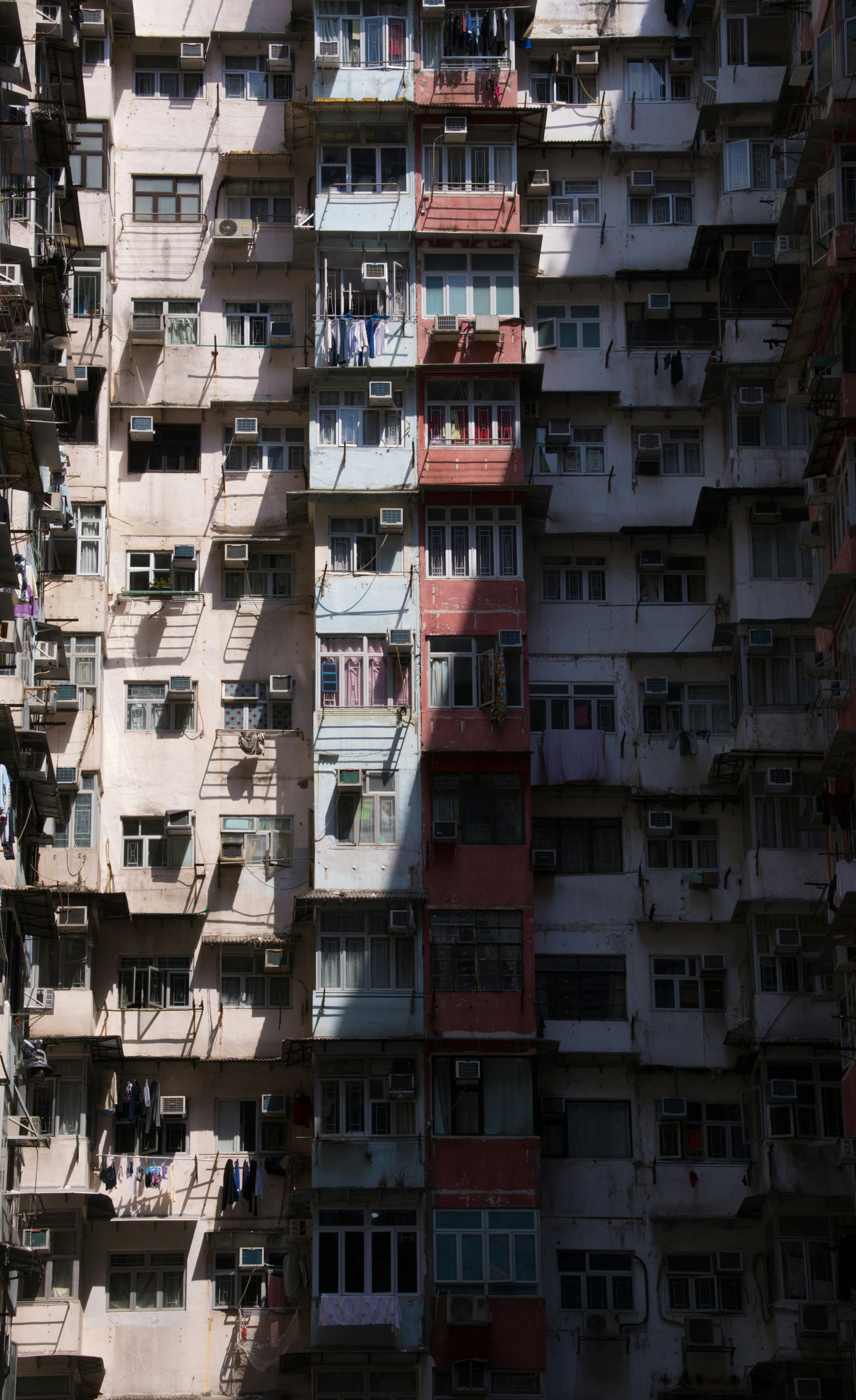 High-rise building facade with alternating sunlight and shadow, highlighting diverse window styles and air conditioning units.