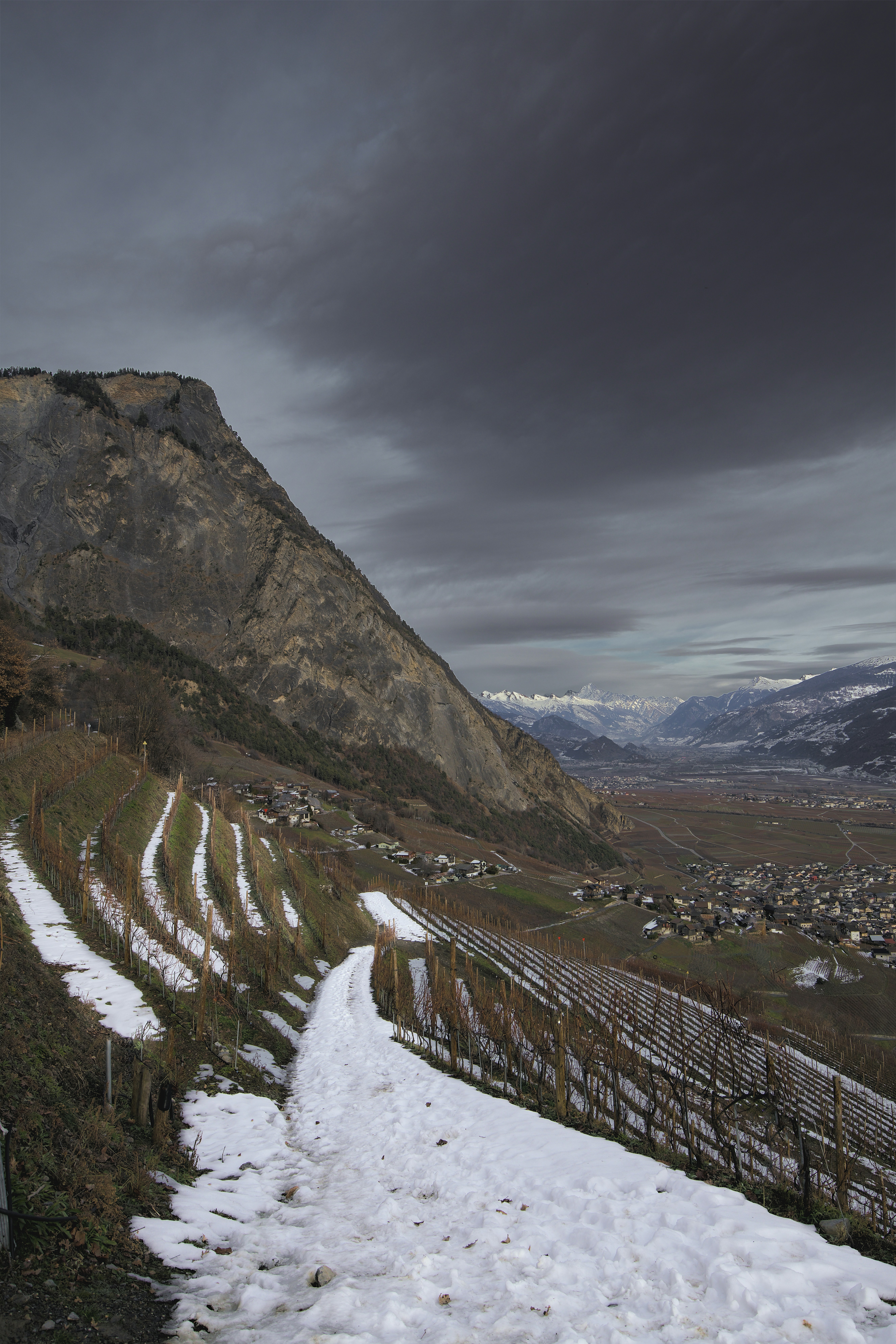 Terraced Snowfields Ascend Toward a Cliffside Valley Under a Moody Sky
