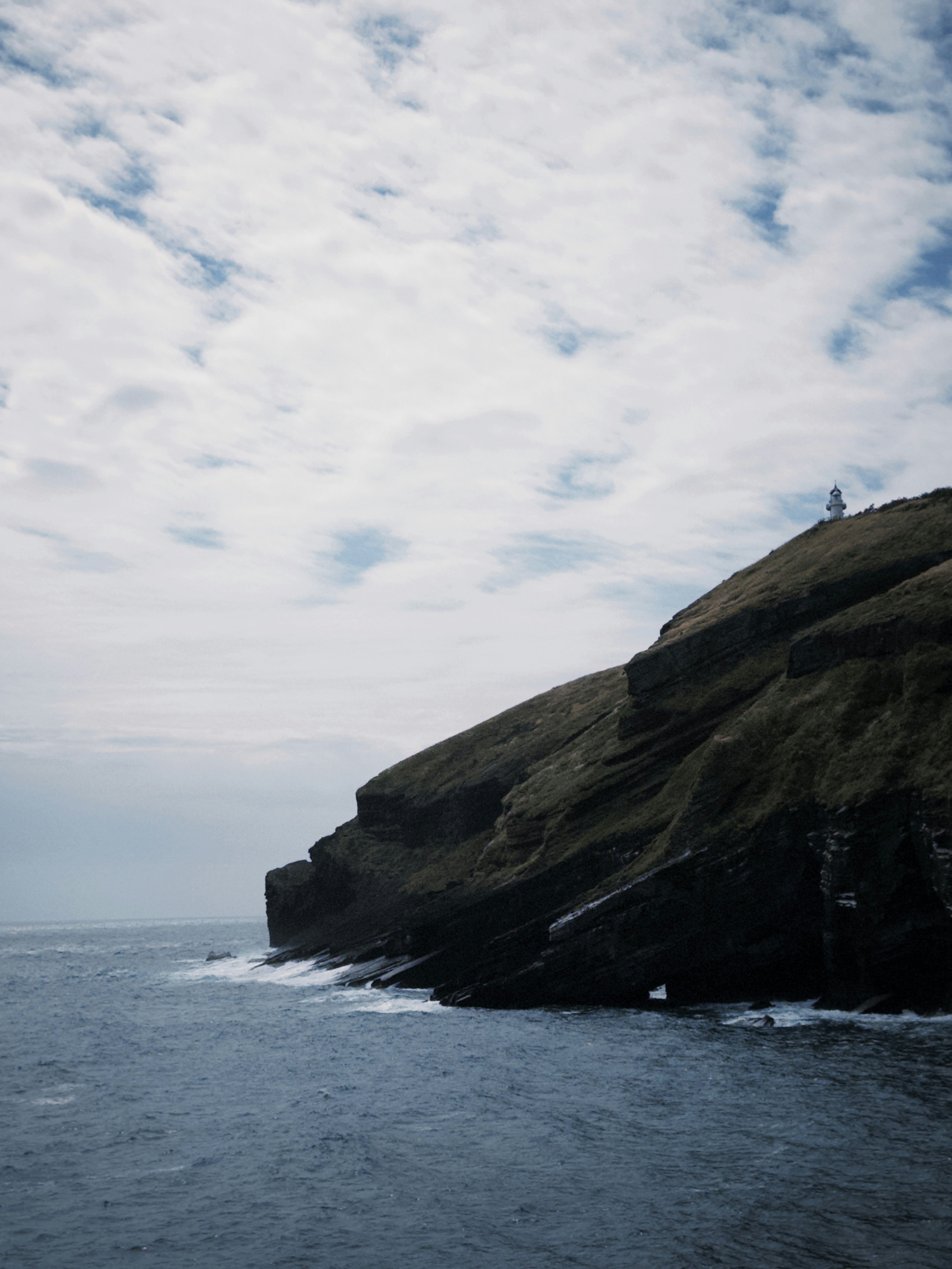 A cliff meets the ocean under a cloudy sky. photo – Free Land Image on ...