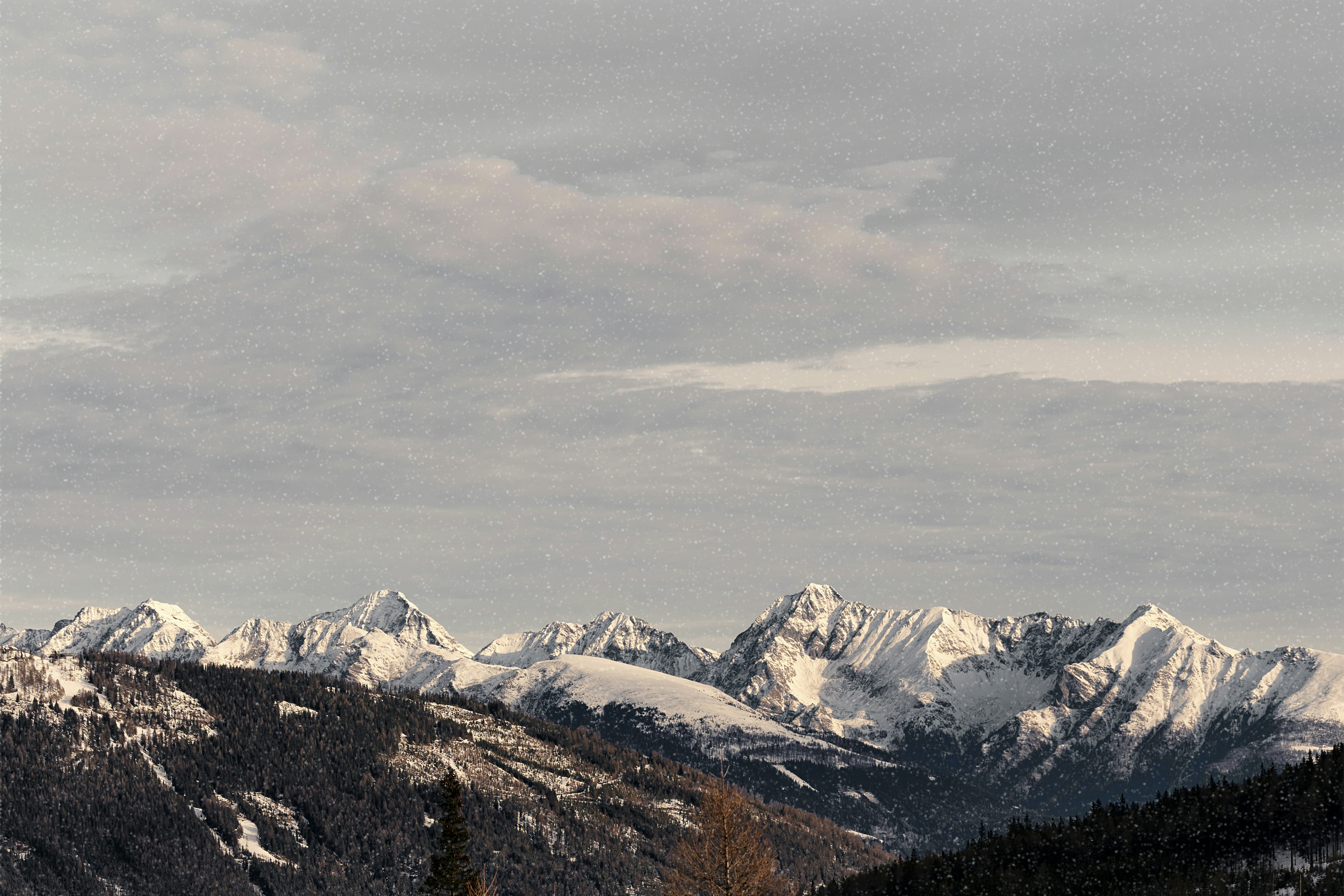 Snow-capped mountain range stretches beneath a cloudy sky.