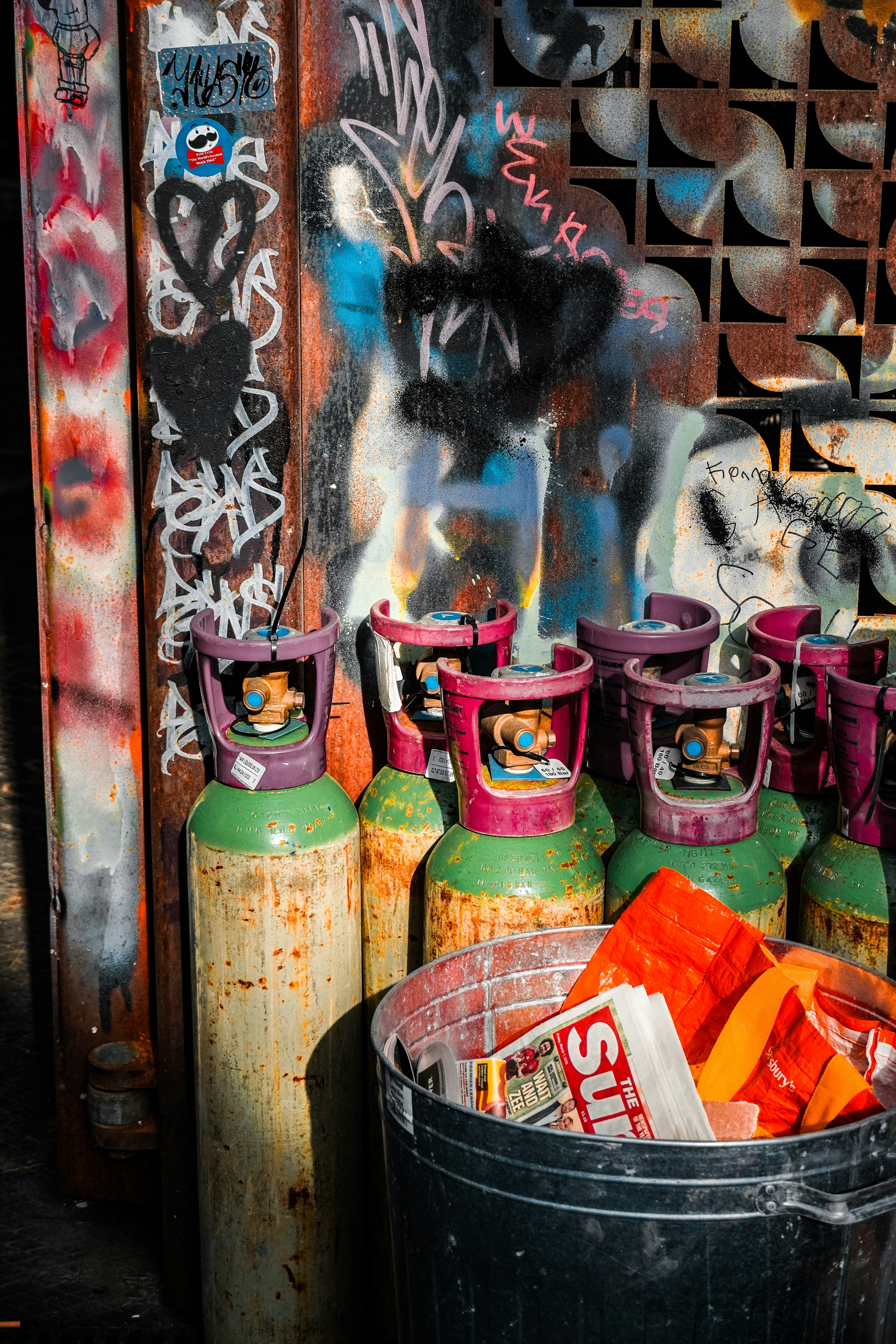 Pink-Valved Gas Cylinders Stand Against a Graffiti-Splashed Wall