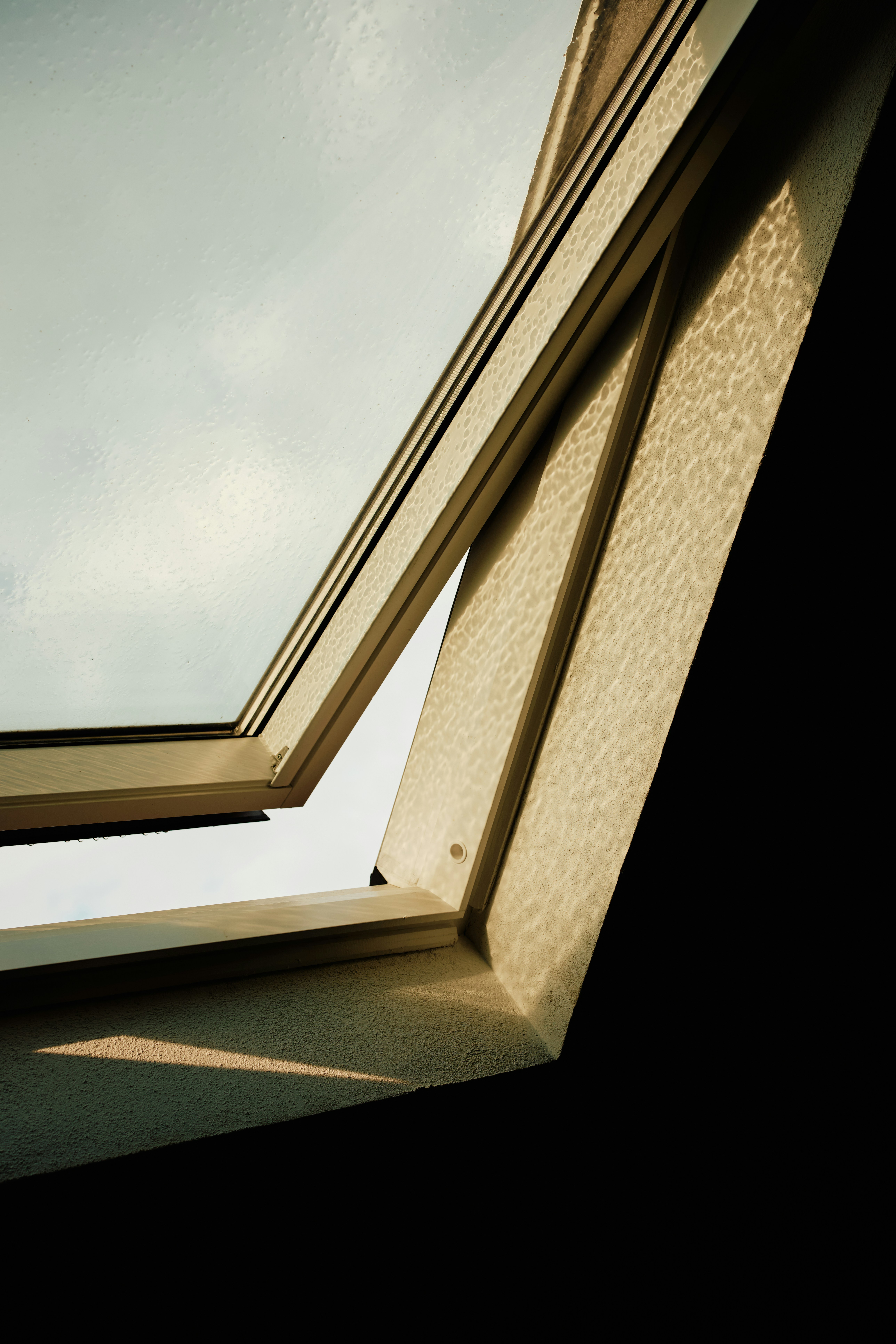 A close-up view of a skylight window with condensation and soft sunlight casting delicate shadows on the wall.