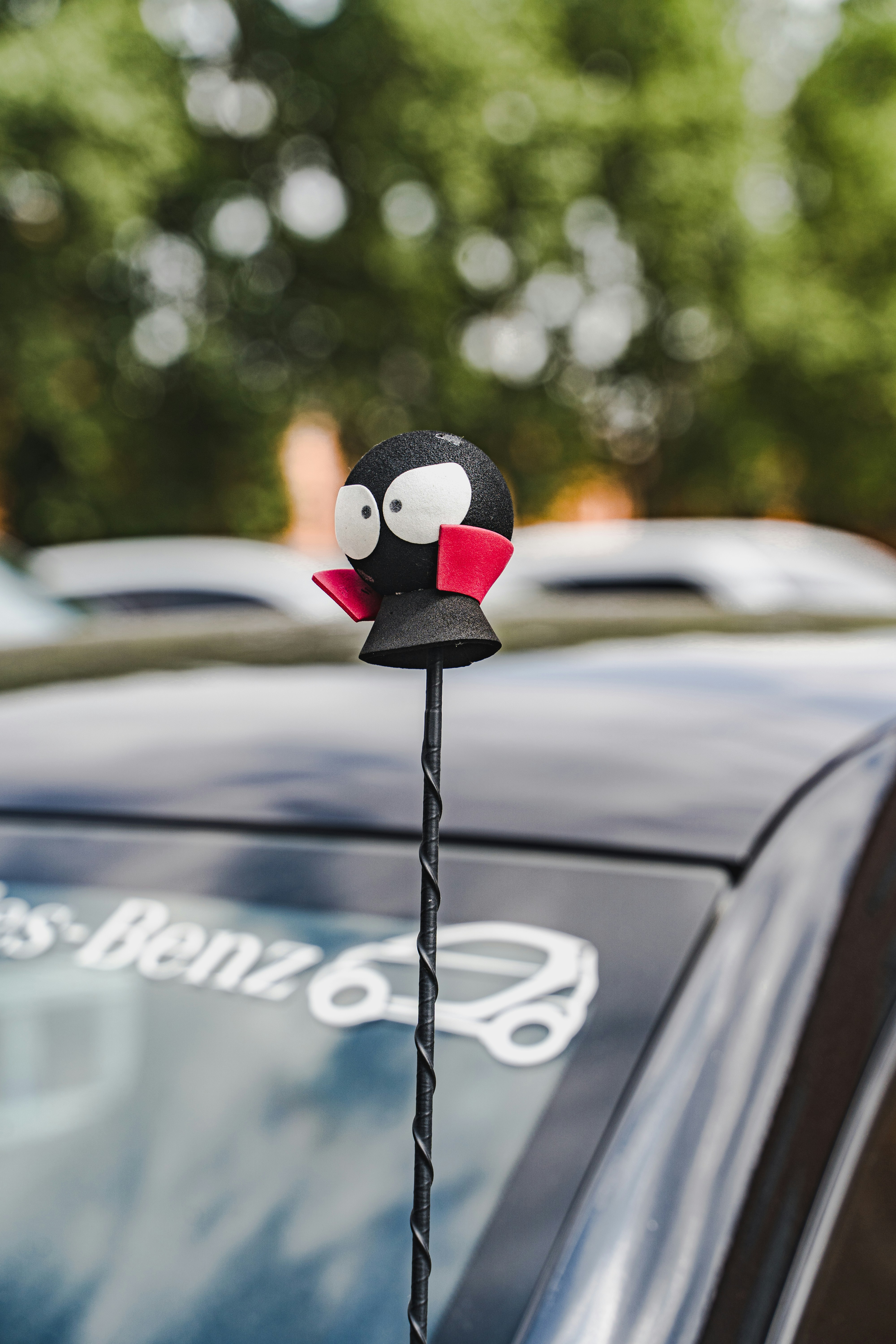 Tiny Sentinel on a Car Antenna: A Cartoon Figure in a Parking-Lot Moment