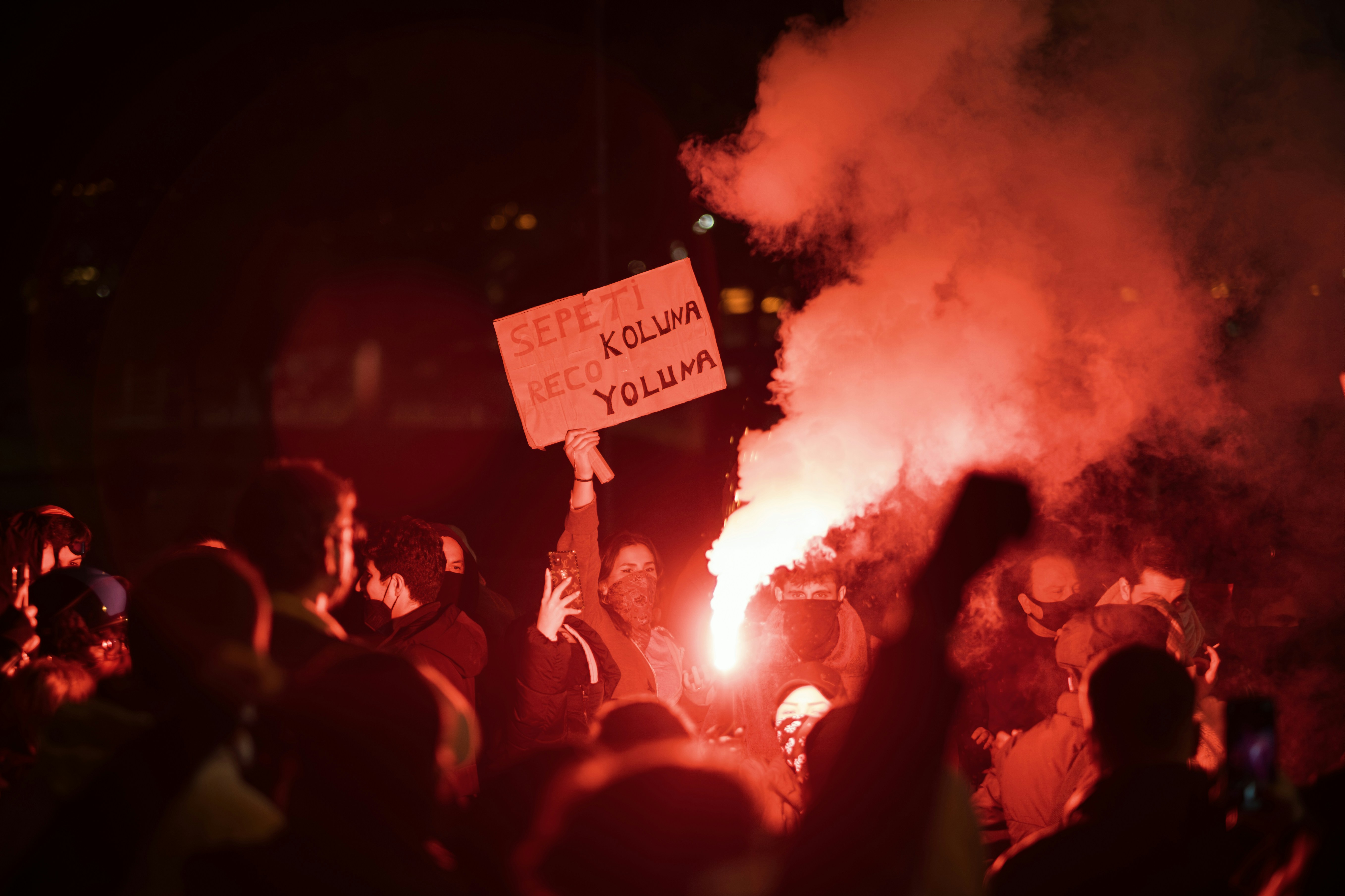 Protestors rally with flares and signs at night. photo – Free People ...