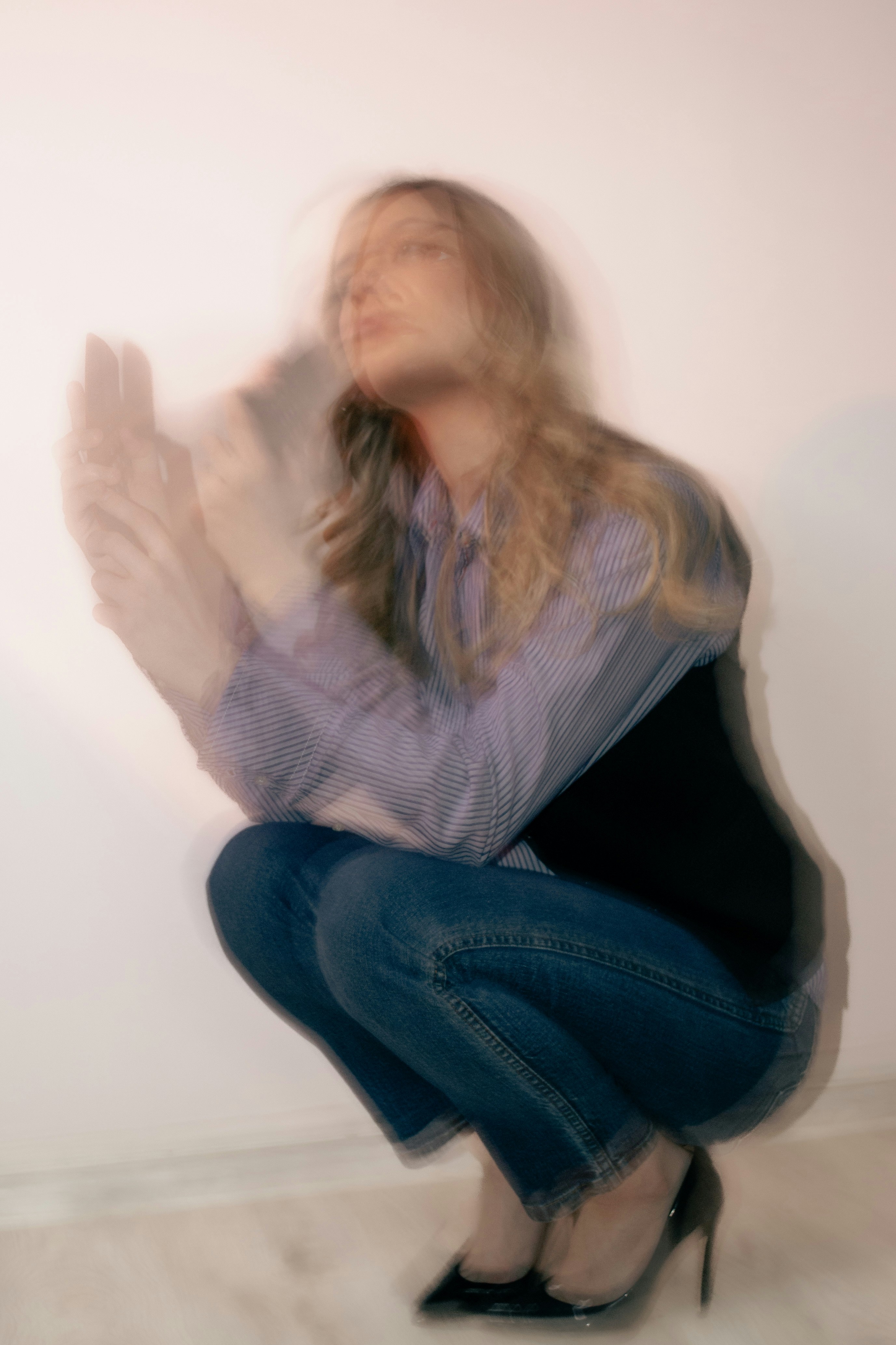 A blurred figure crouching with a phone, embodying movement and modernity against a soft backdrop.