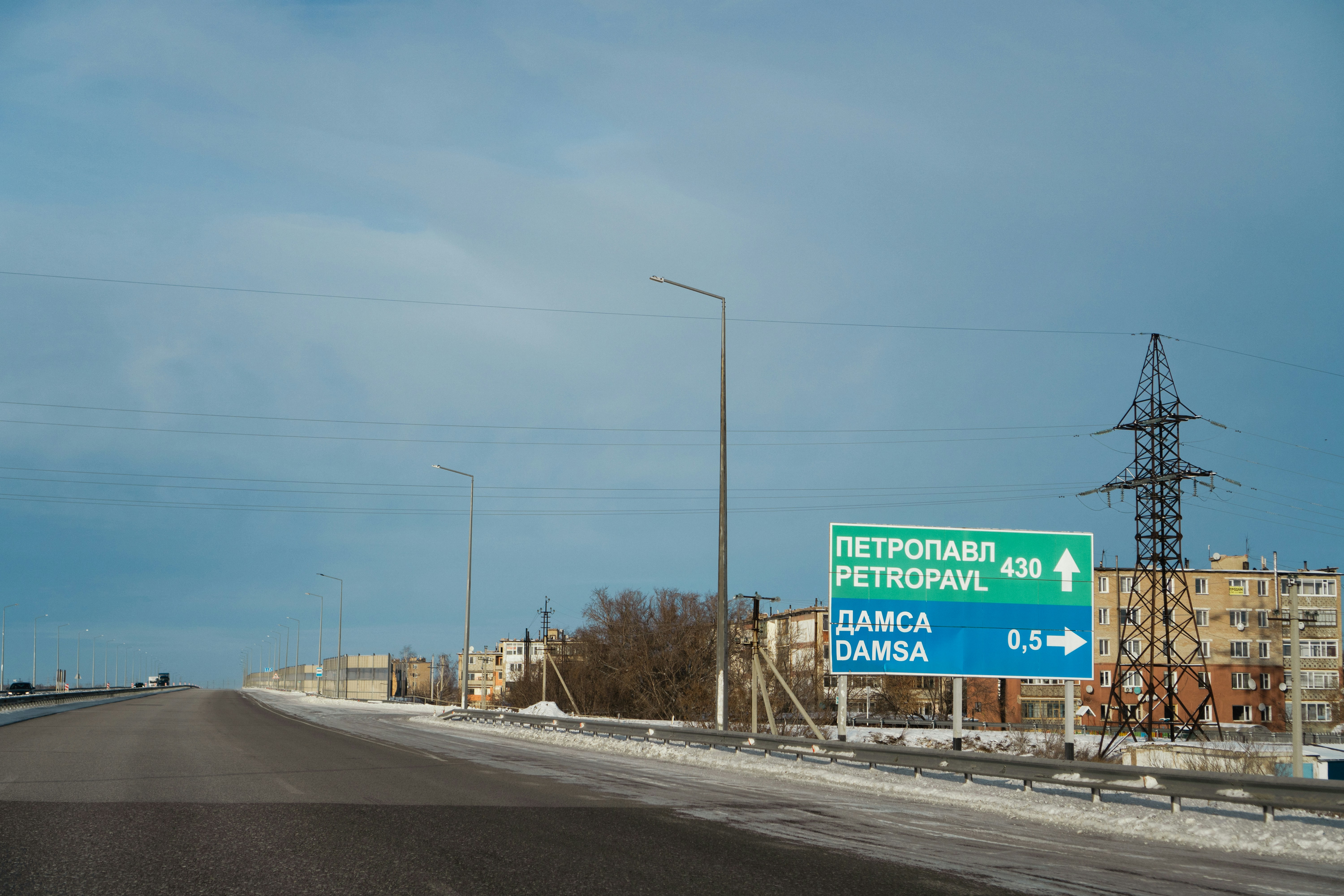 Open highway stretching towards distant buildings with a sign indicating directions under a vast sky.