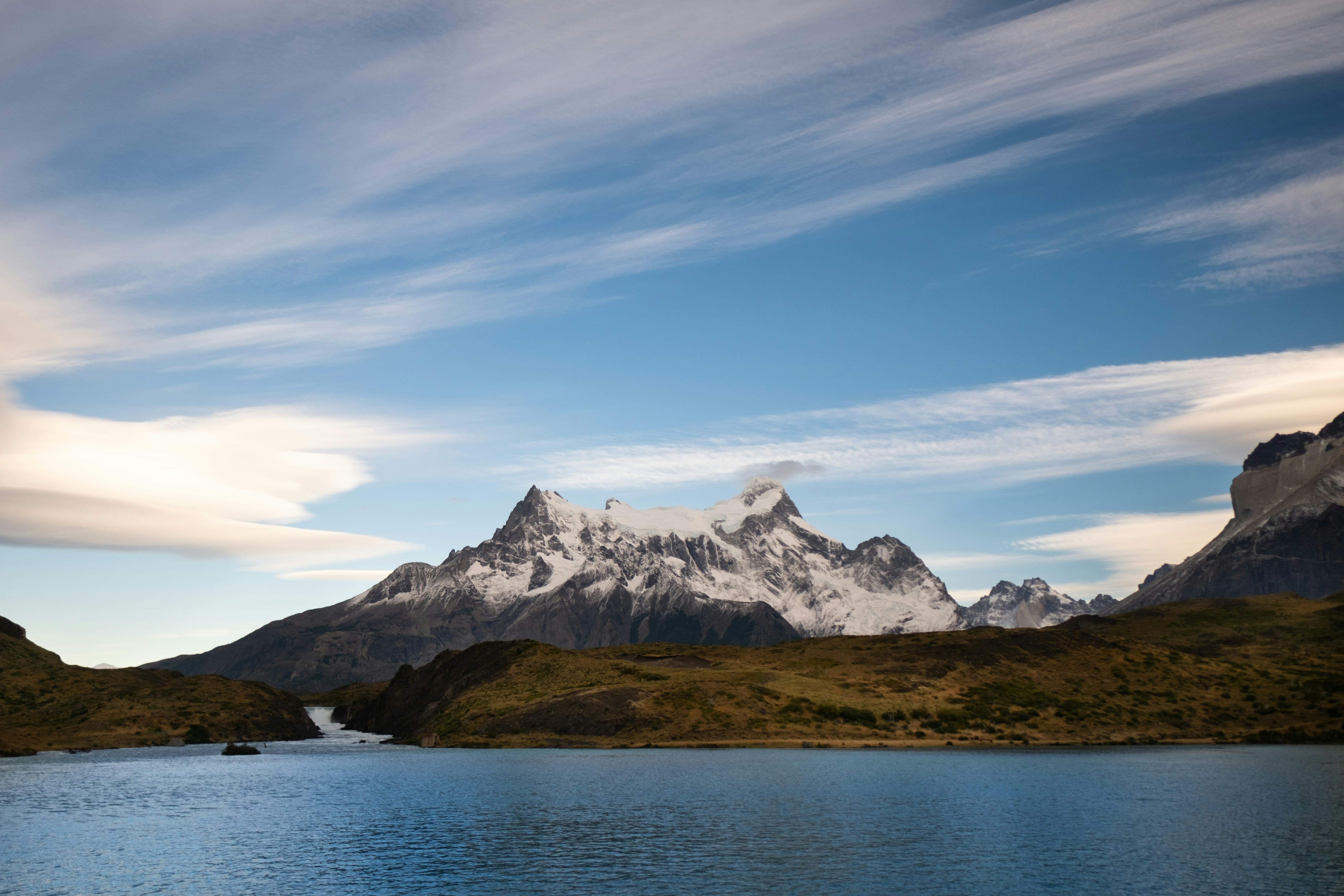 Snow-capped mountains under a dynamic sky reflected in a tranquil lake.