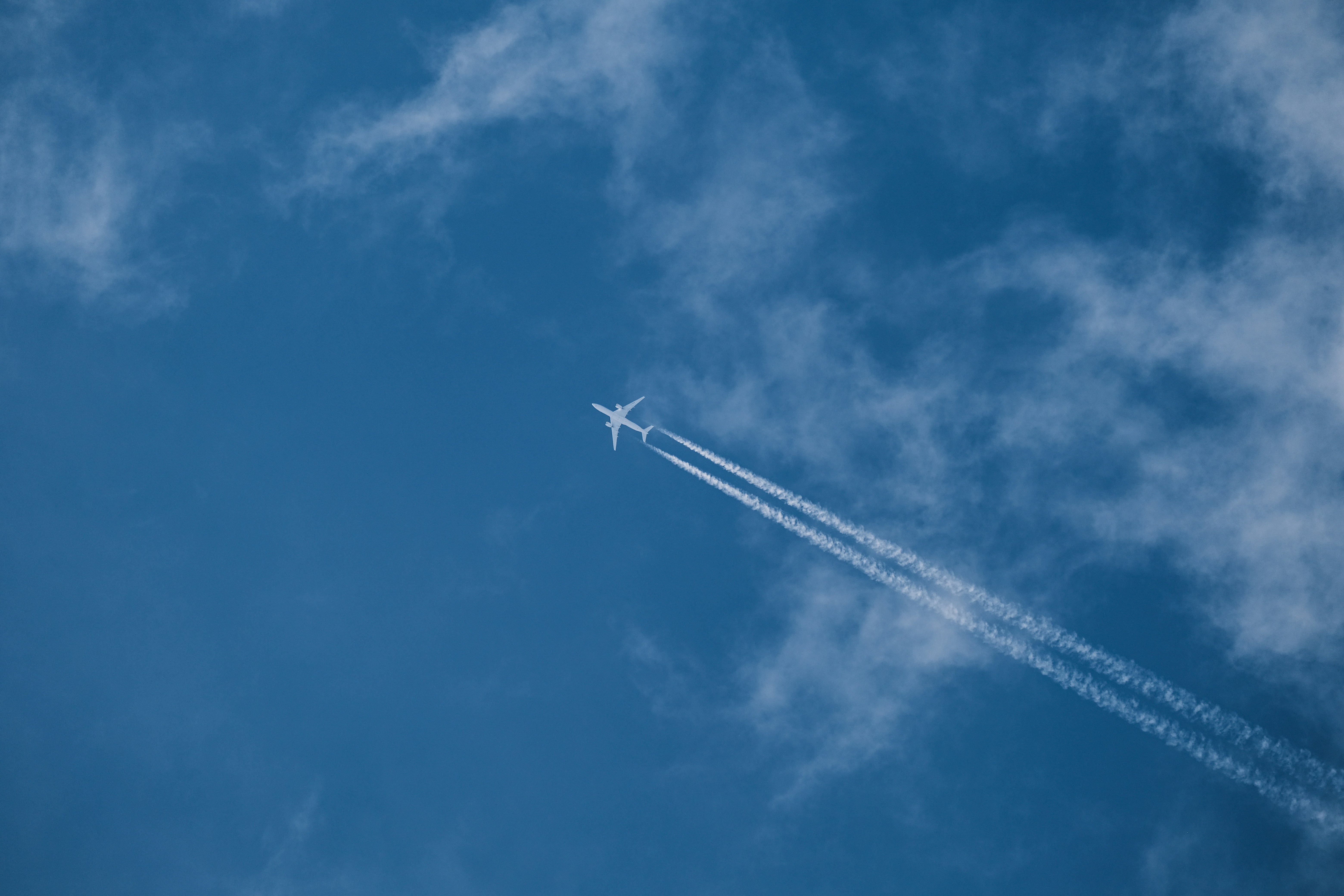 Jet airplane soaring through a clear blue sky, leaving contrails as it passes soft, wispy clouds.