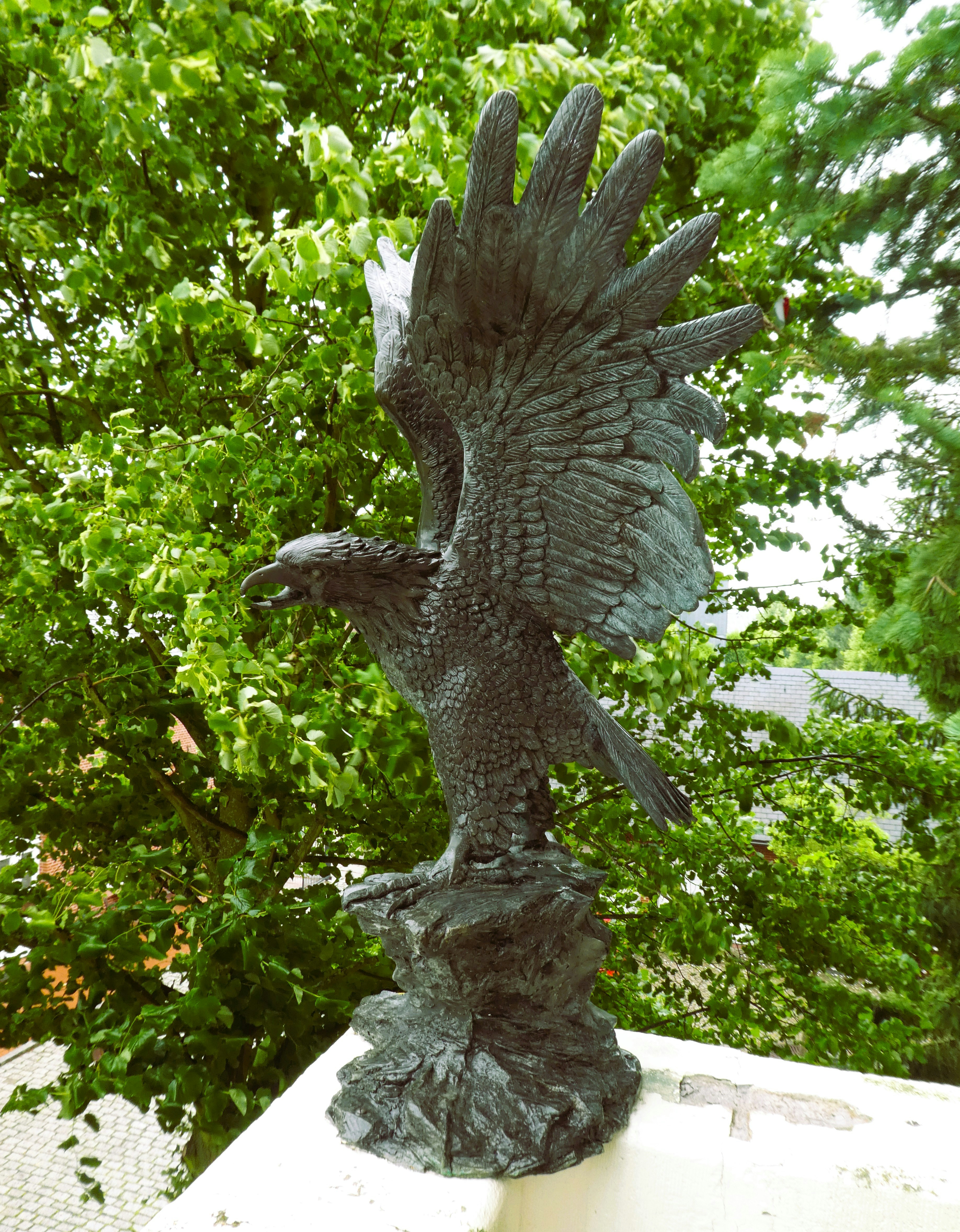 Bronze eagle sculpture poised for flight, set against a backdrop of lush green foliage.