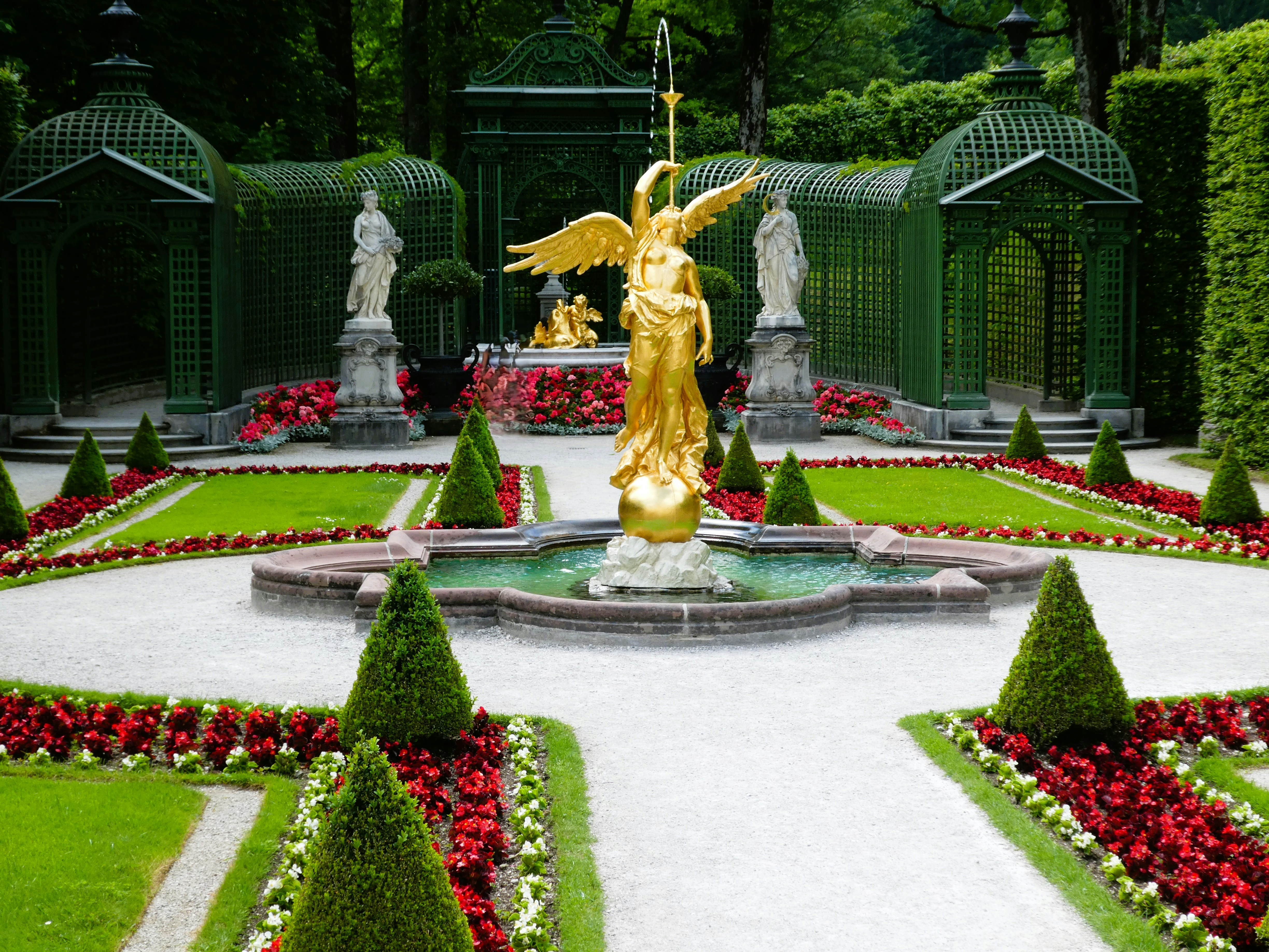 Ornate garden with a golden statue centerpiece surrounded by manicured hedges and vibrant flowerbeds.