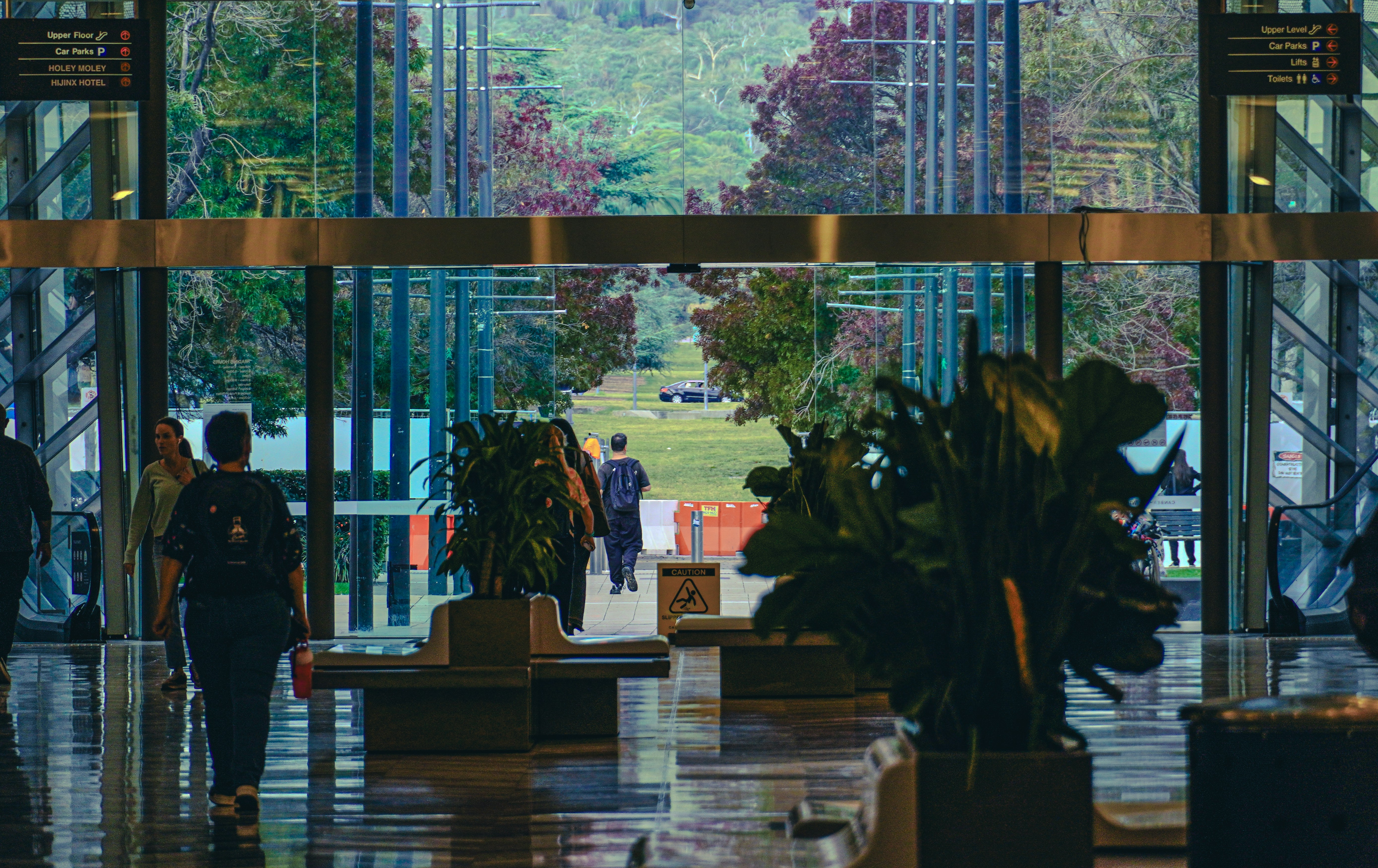 A view of the outdoor landscape through a glass entrance, with people walking inside the building.