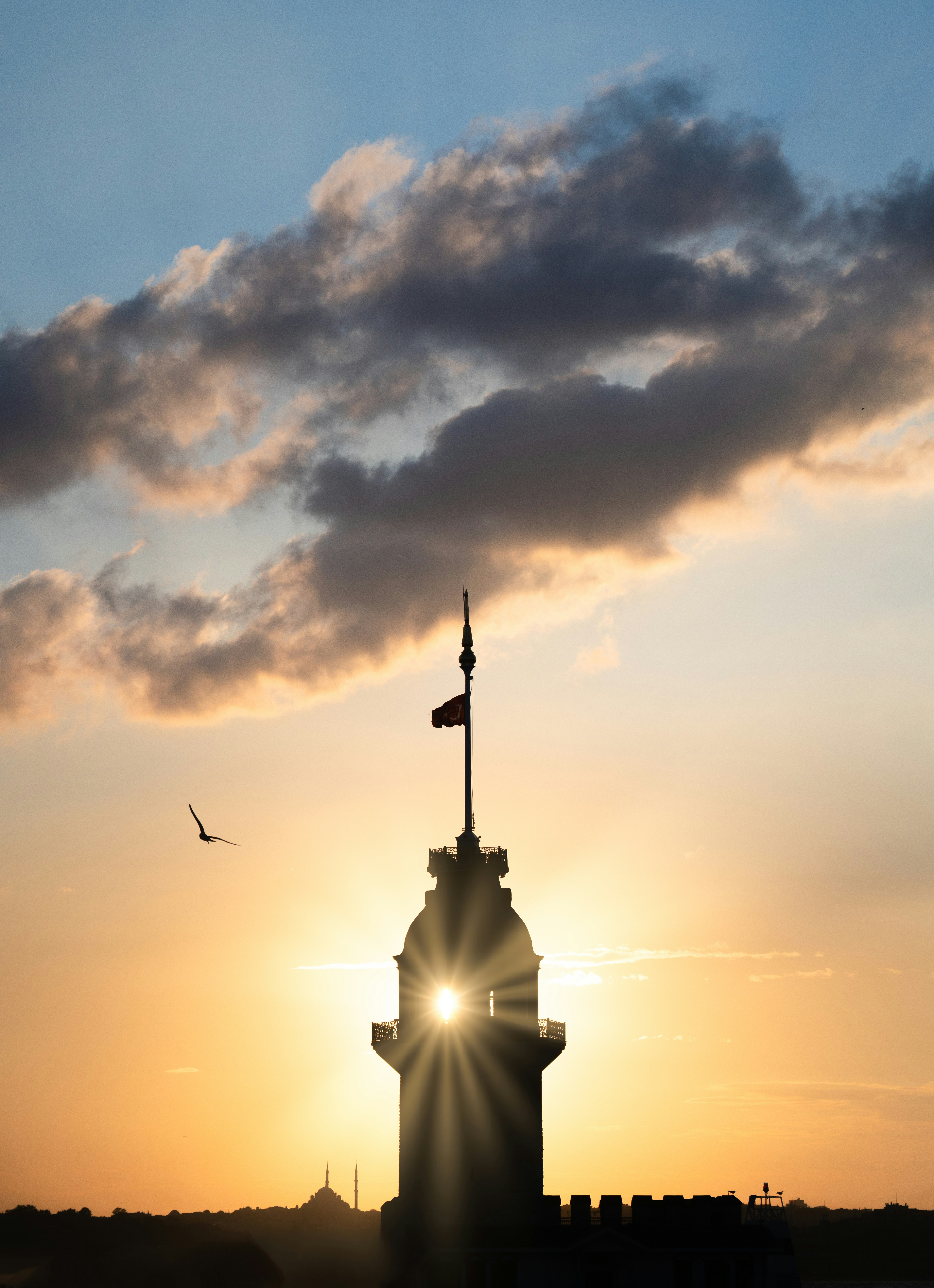 Silhouette of a tower with a flag against a vibrant sunset sky, a bird soaring nearby.