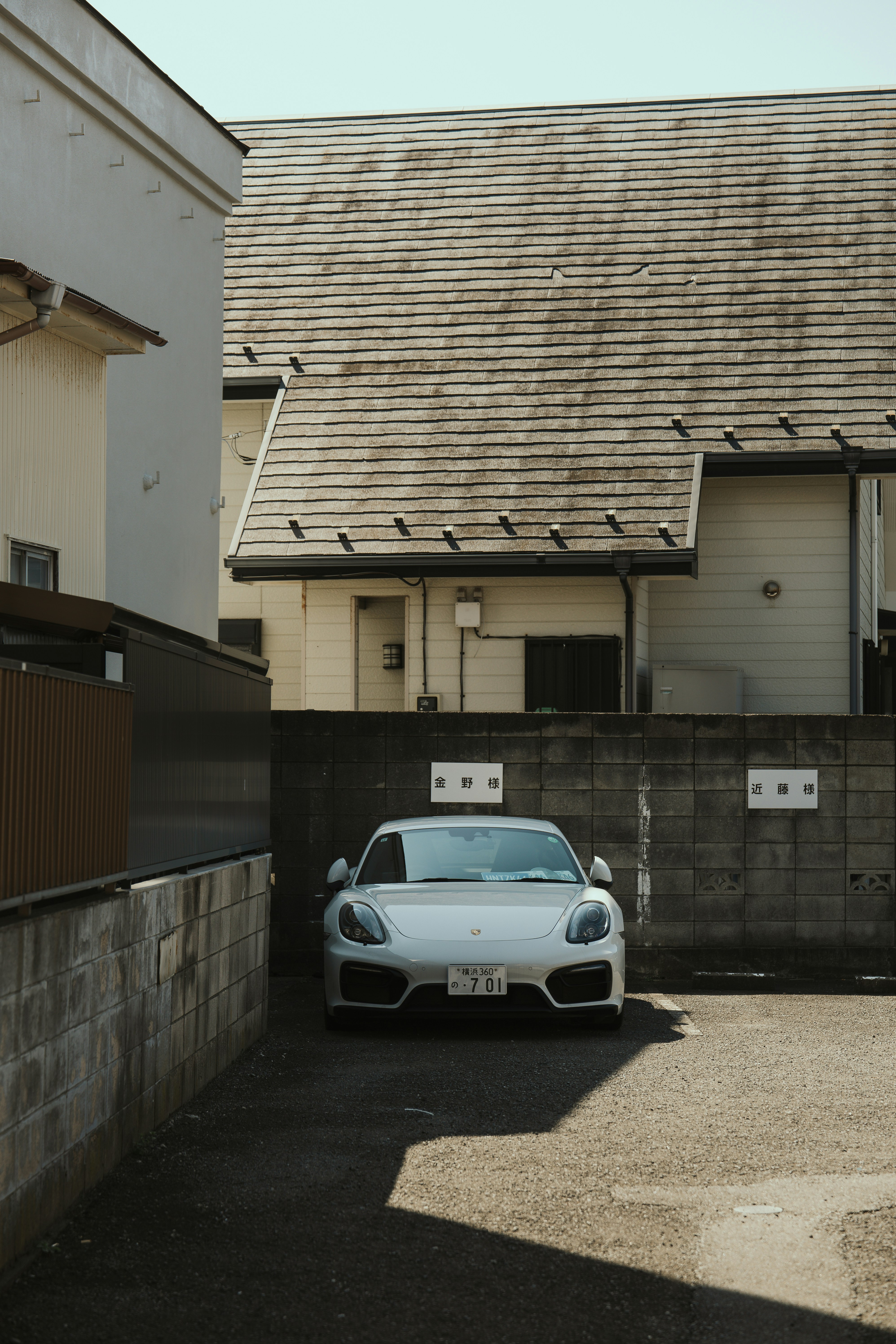 White sports car parked in a narrow alleyway between concrete walls under a clear sky.