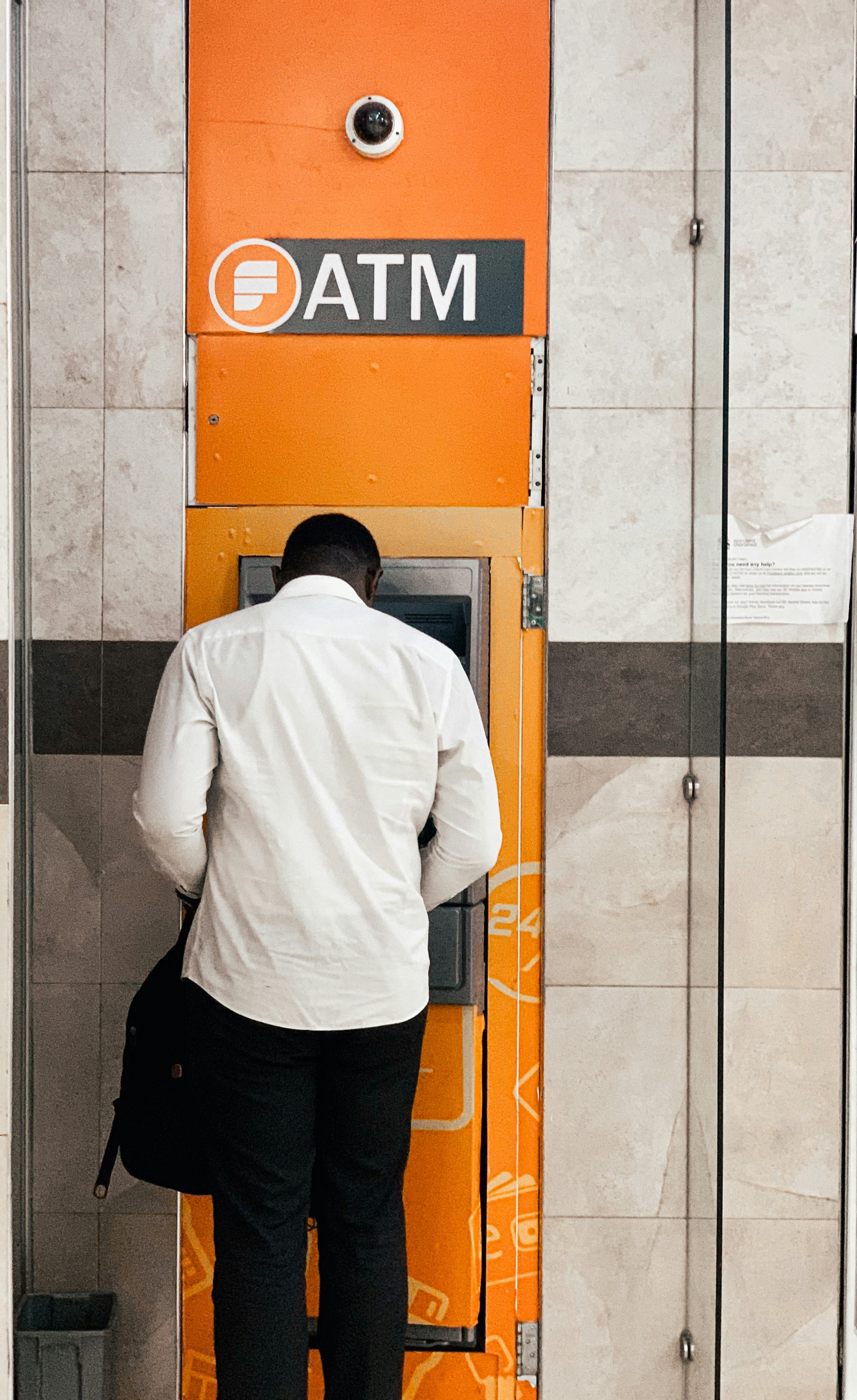 A man uses an atm in an orange kiosk. photo – Free Man Image on Unsplash