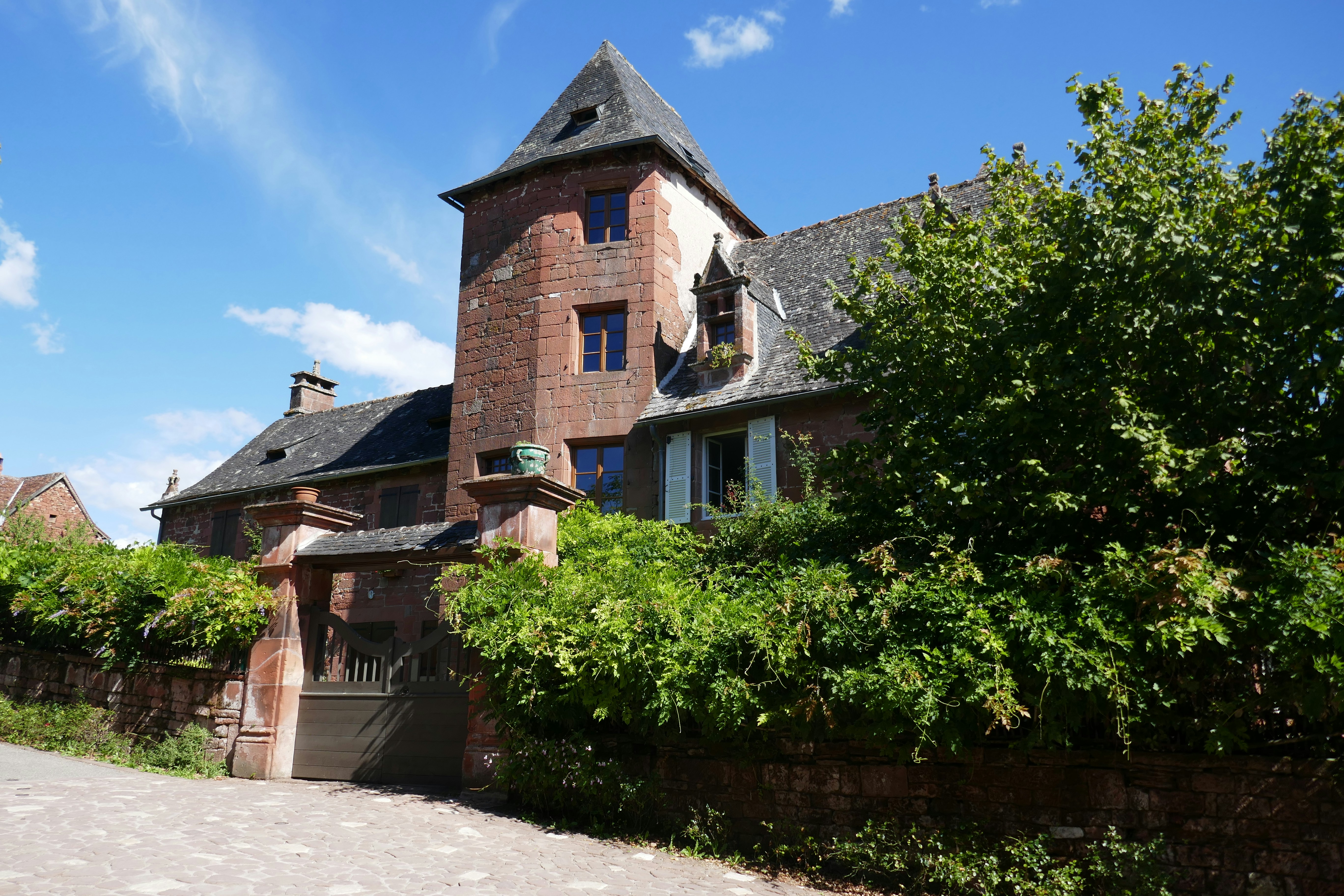 Historic brick building with a tower, surrounded by lush greenery under a clear blue sky.