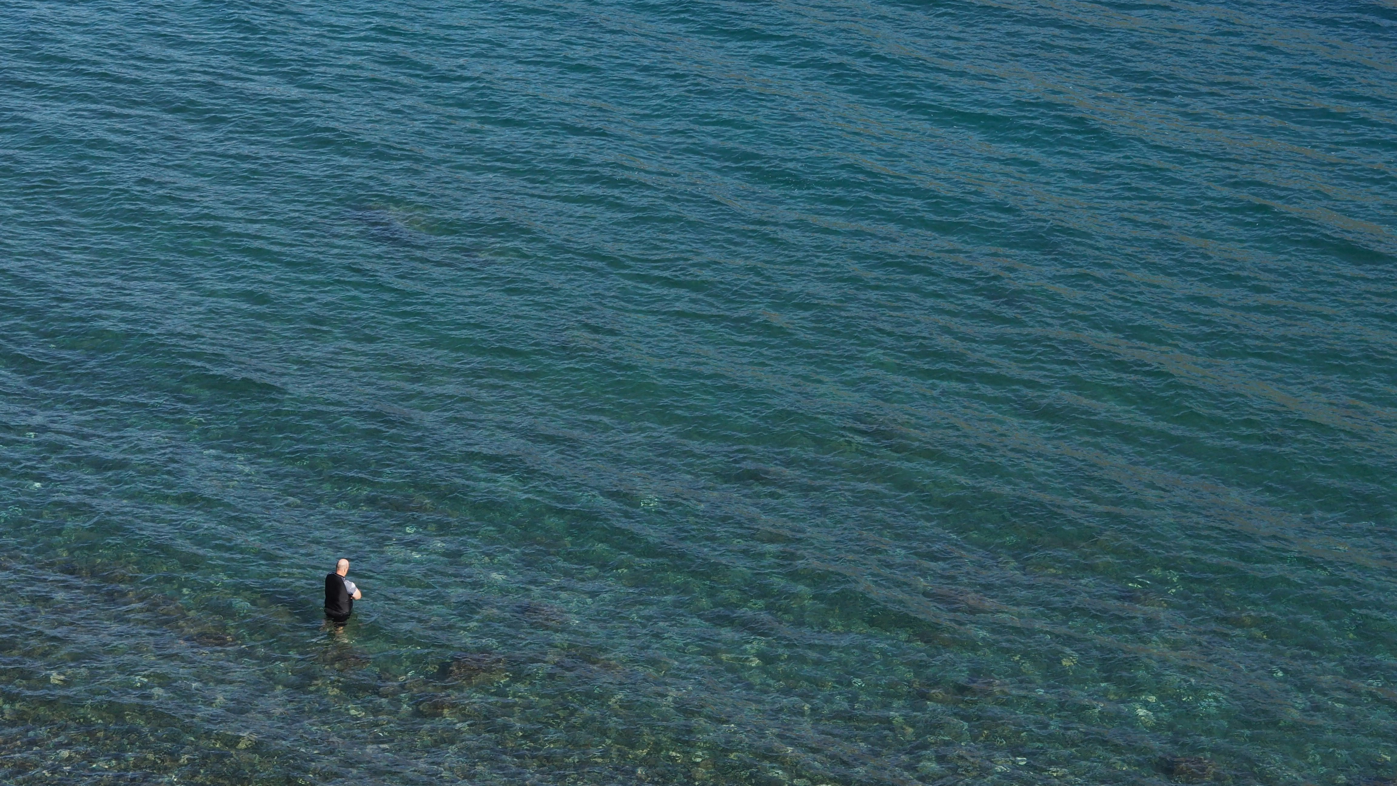 Person stands alone in the clear, blue waters of Lake Wakatipu.