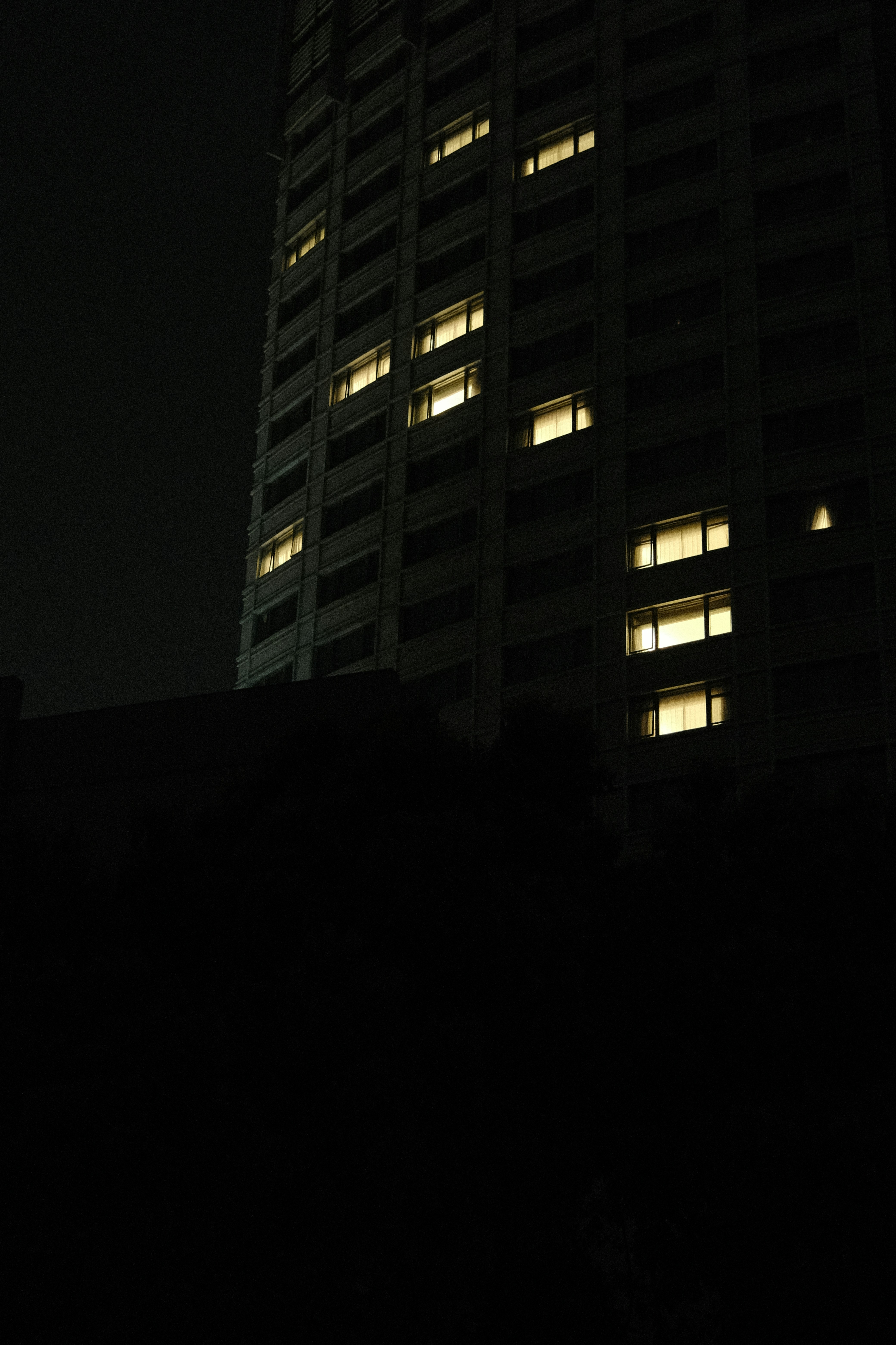 A high-rise building at night, featuring illuminated windows against a dark backdrop, hinting at the lives within. 