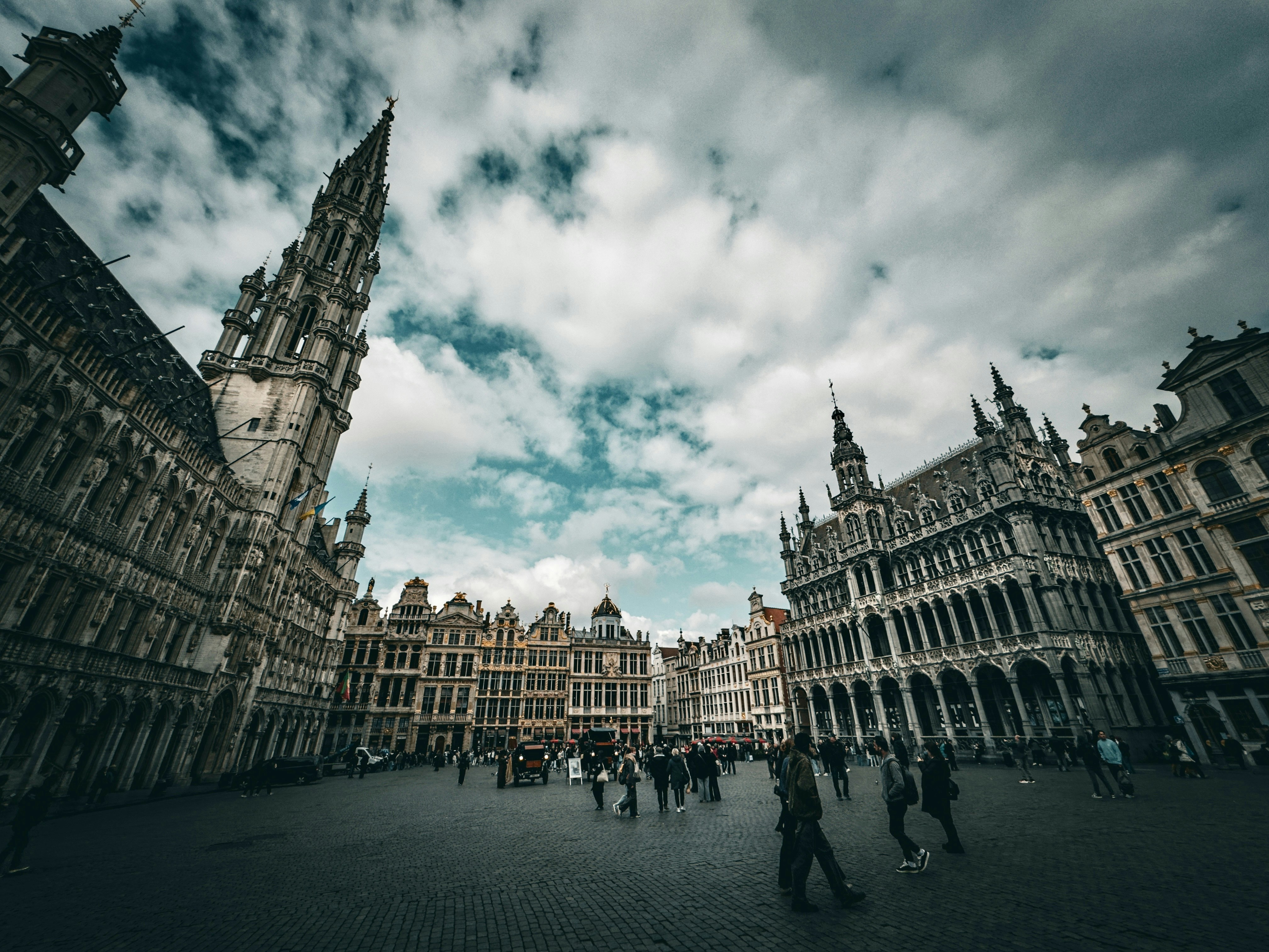 Gothic-style Town Hall and ornate King’s House frame the bustling cobblestone Grand Place in Brussels beneath a dramatic sky.