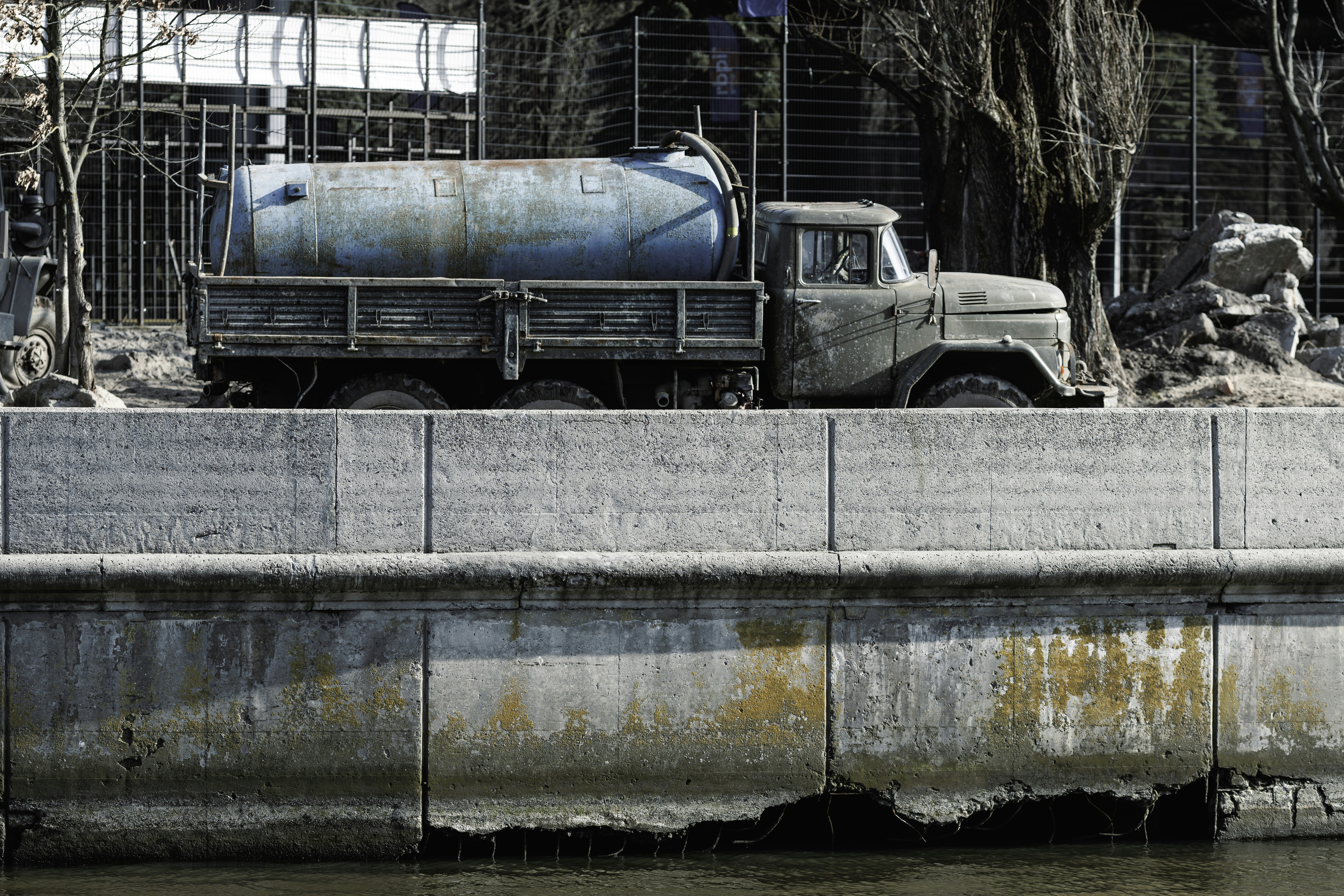 An old, rusty truck sits near a concrete wall.