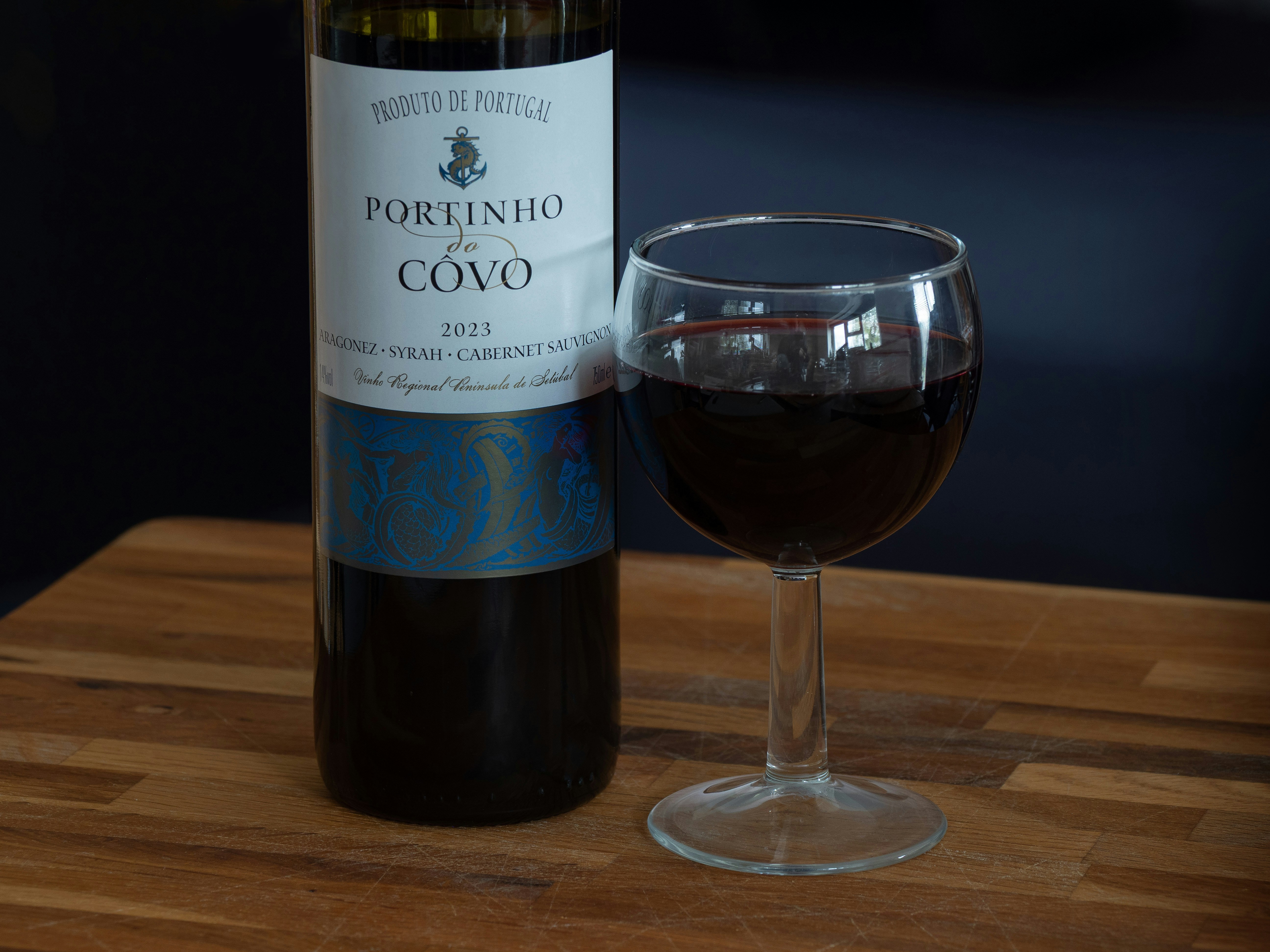 Bottle of Portuguese red wine beside a filled glass on a wooden surface.