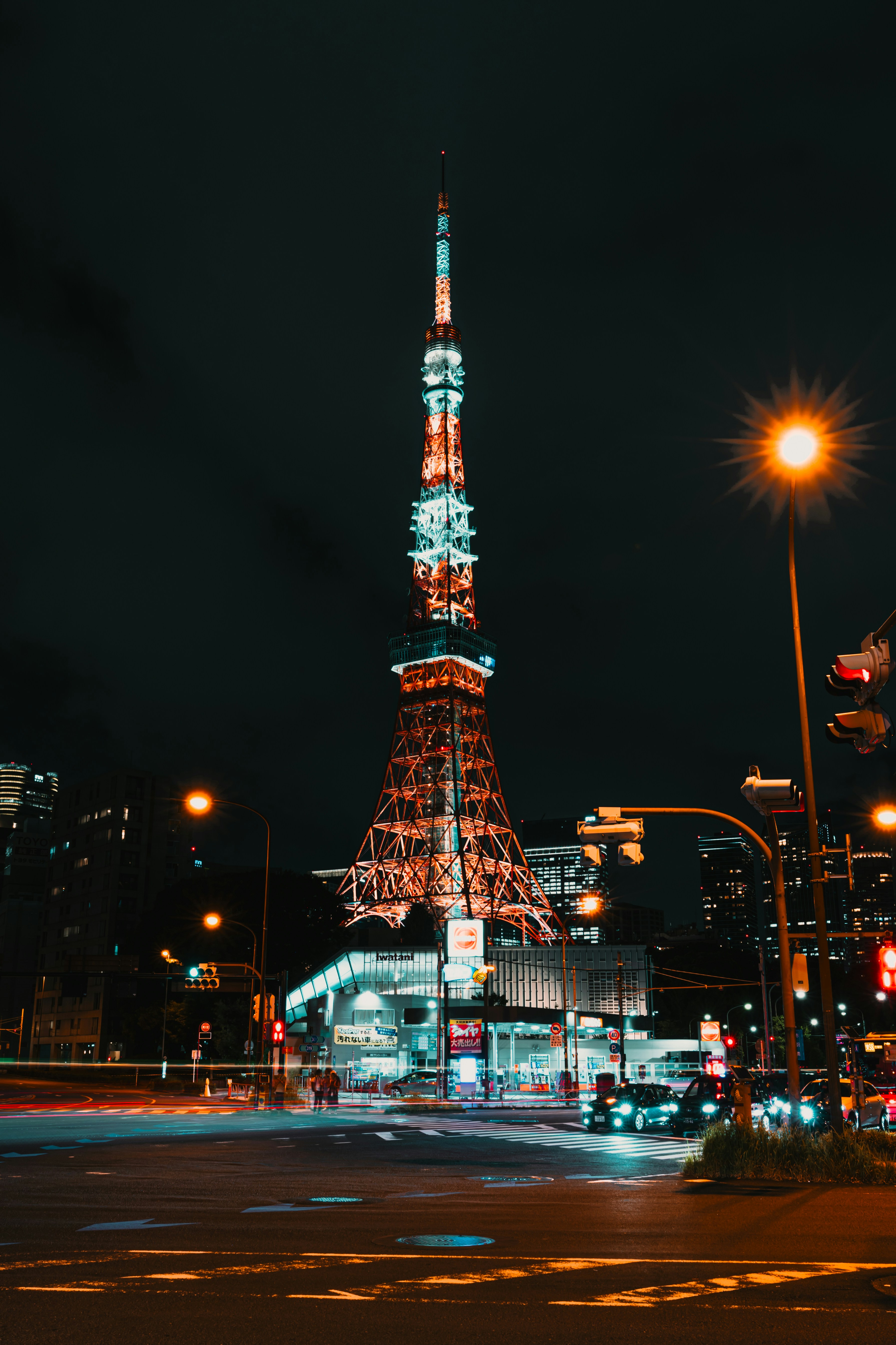 Tokyo Tower lit up at night, with blurred car light trails and city lights in the foreground.