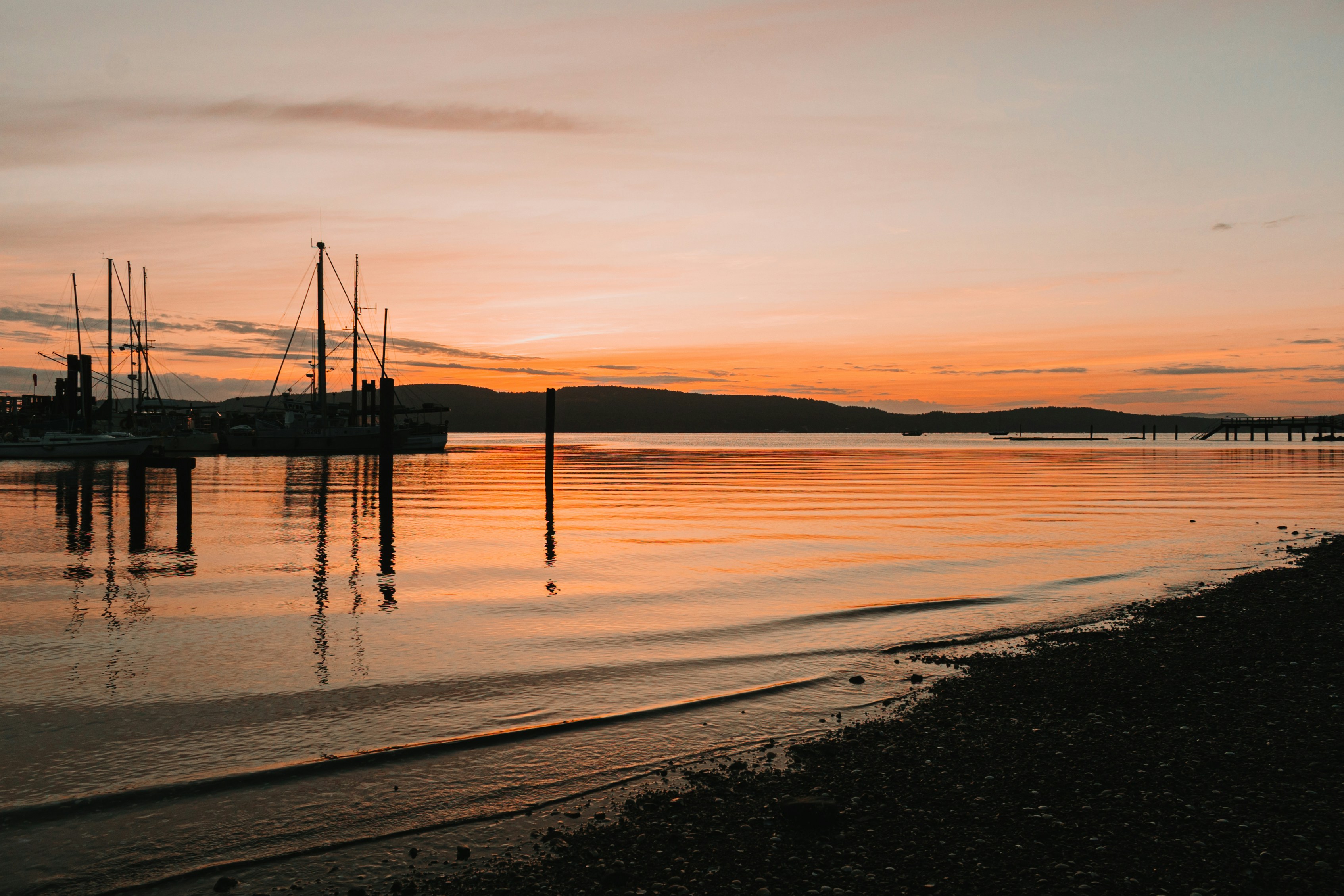 Silhouetted boats in a tranquil harbor with a vibrant orange sunset reflected on the water.