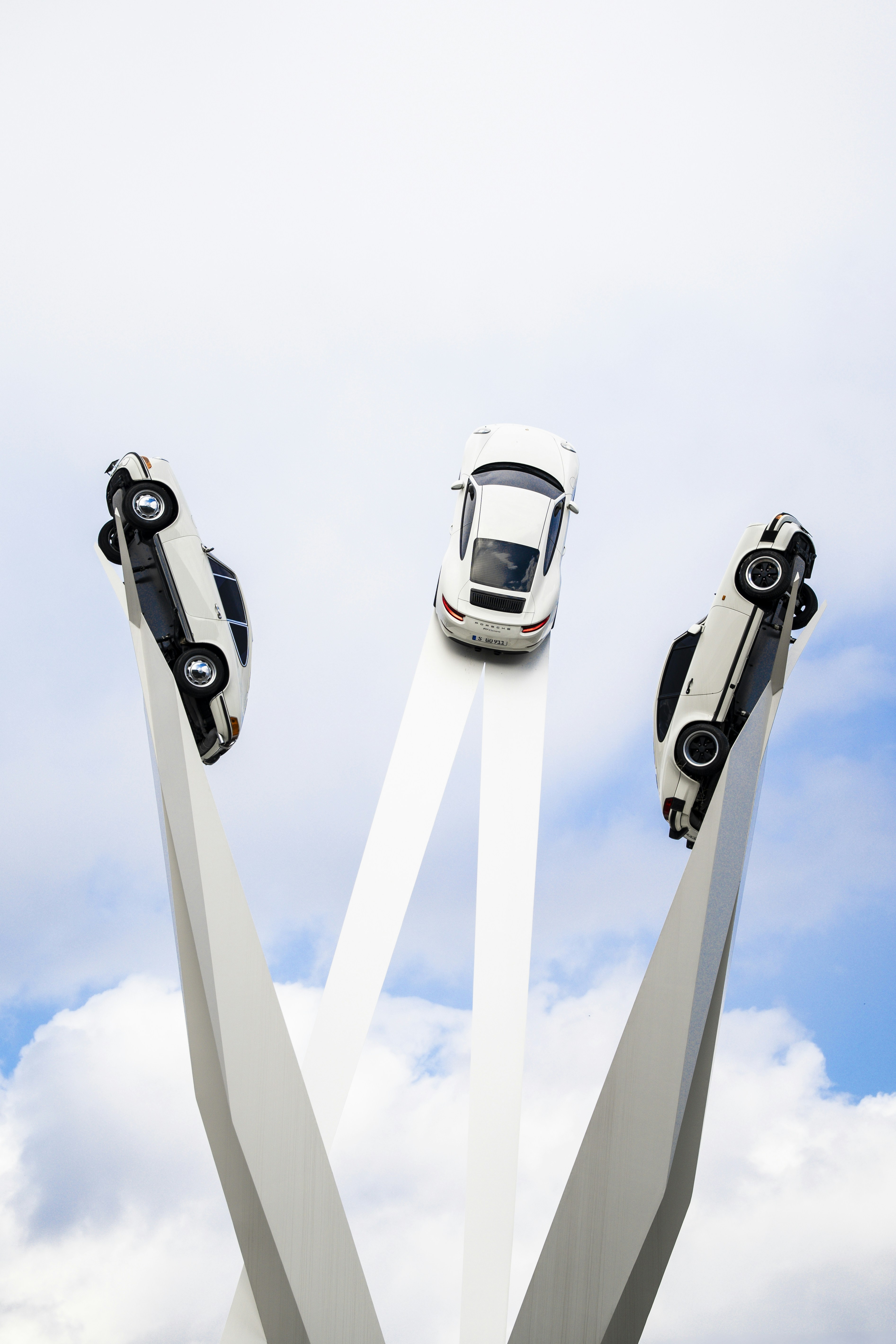 Three rising cars: a skyward sculpture balancing on a steel arc