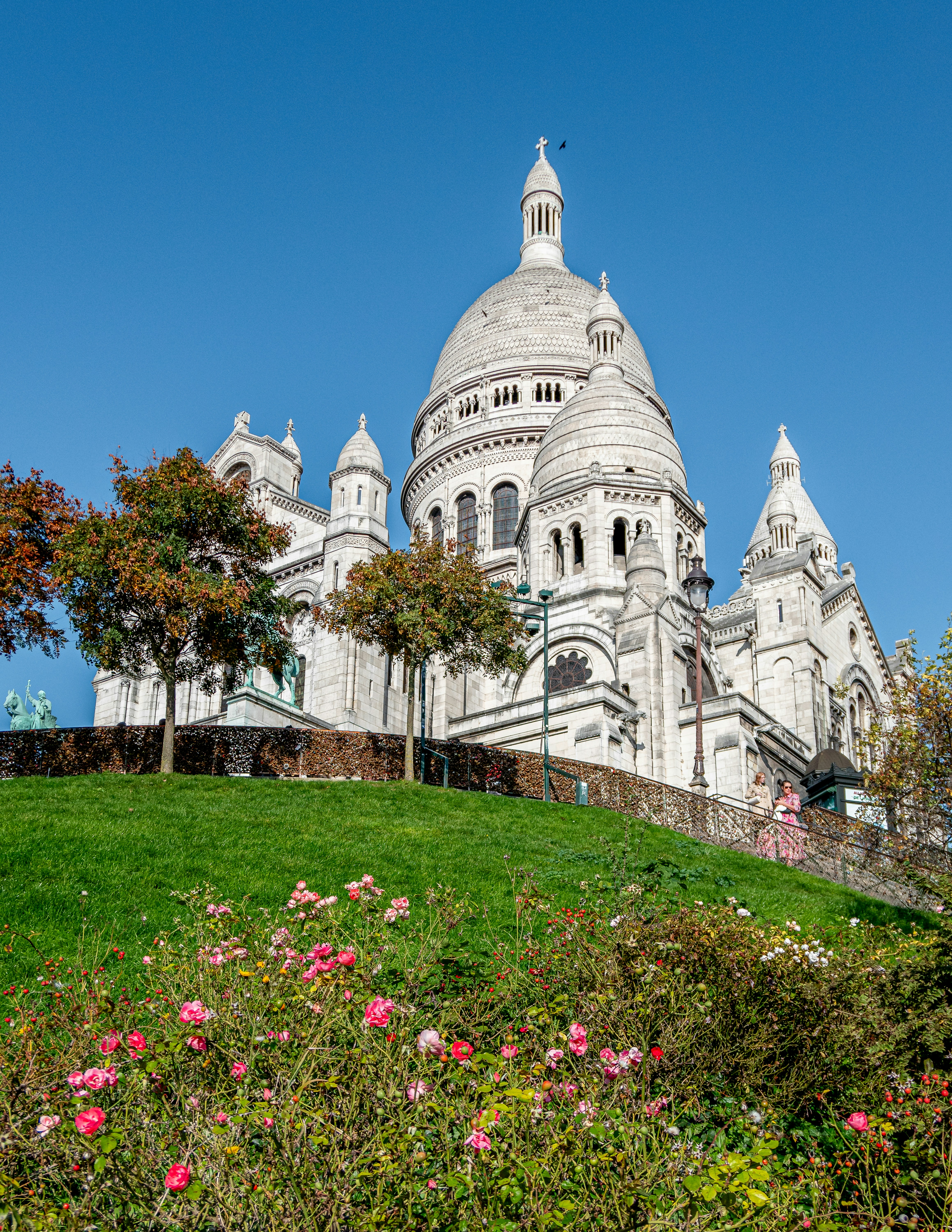 Sacre-Coeur Basilica stands majestically against a clear blue sky, framed by lush greenery and vibrant flowers.