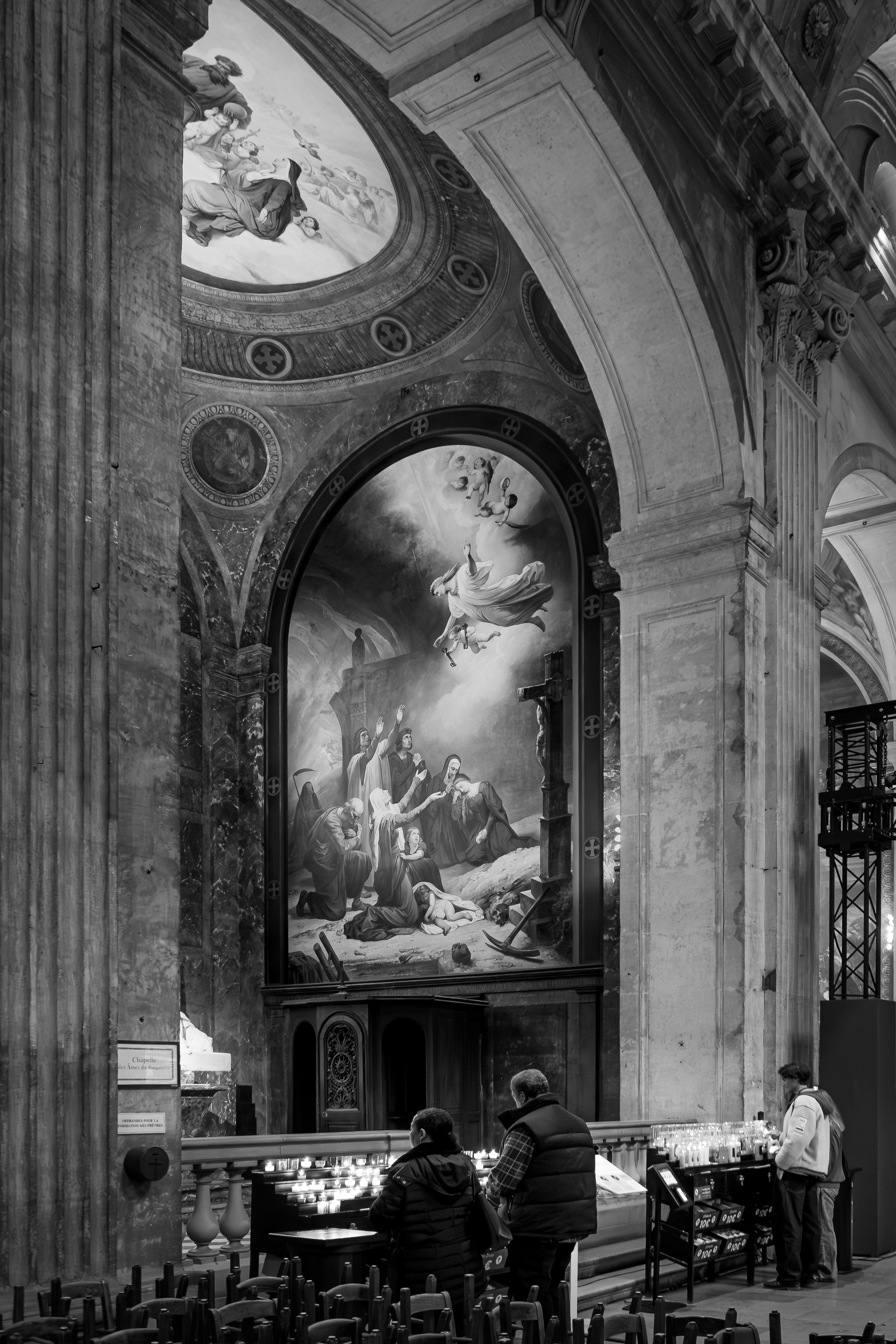 Interior of a grand cathedral with towering columns, ornate arches, and a dramatic painting illuminated by soft light.