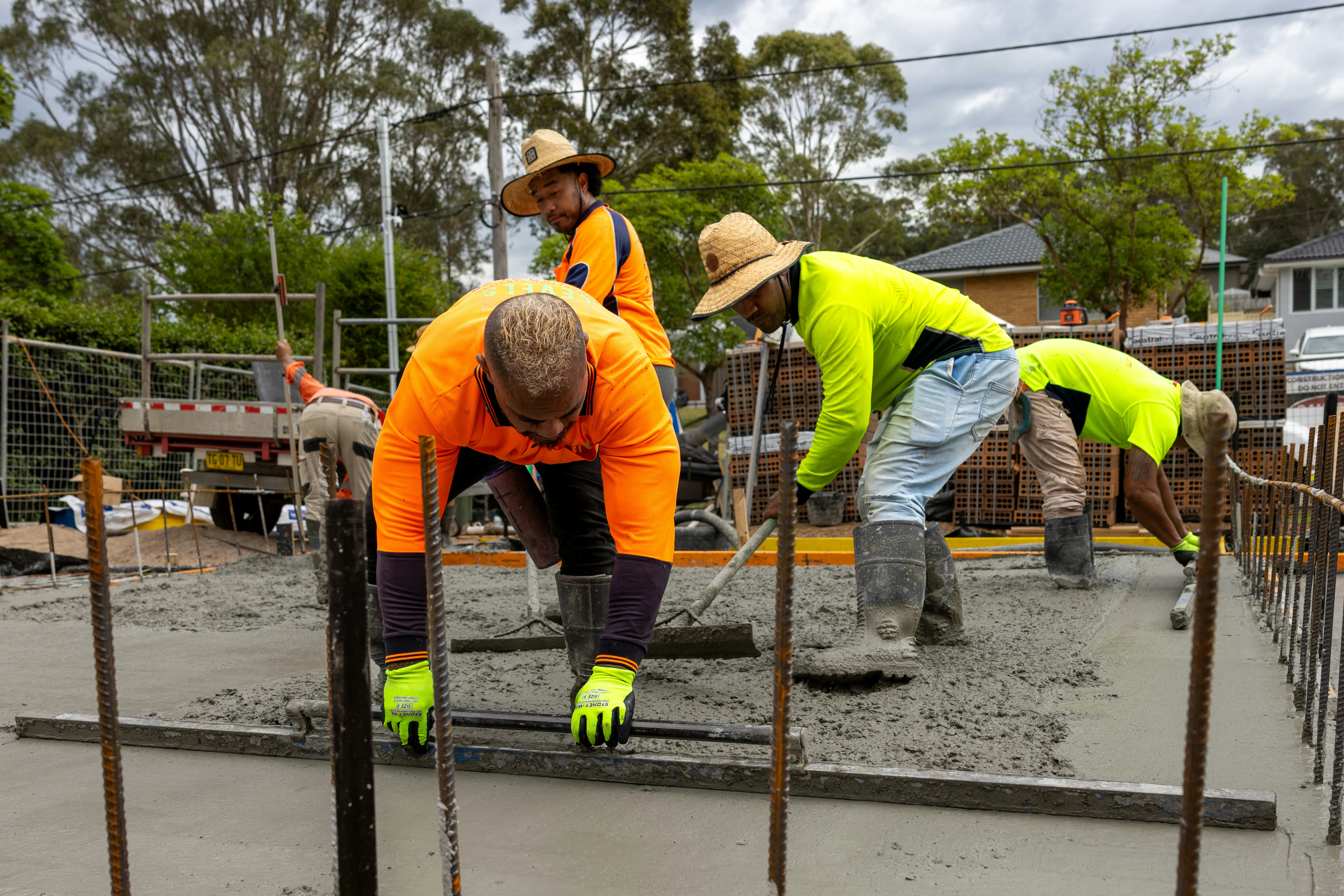 Workers in bright safety gear smoothing freshly poured concrete on a construction site.
