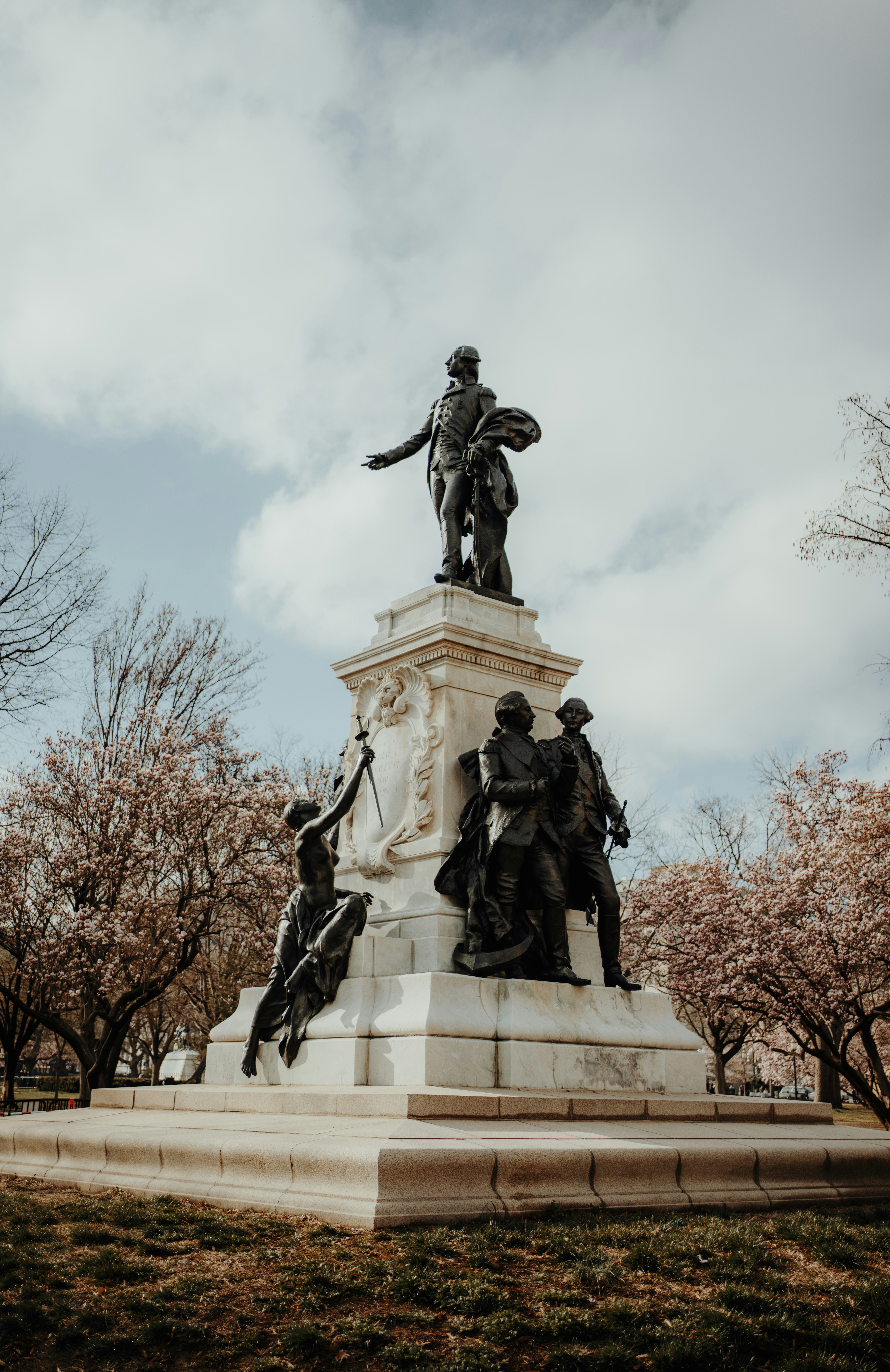 Bronze statue commemorating historical figures, surrounded by blooming cherry trees in a public park.