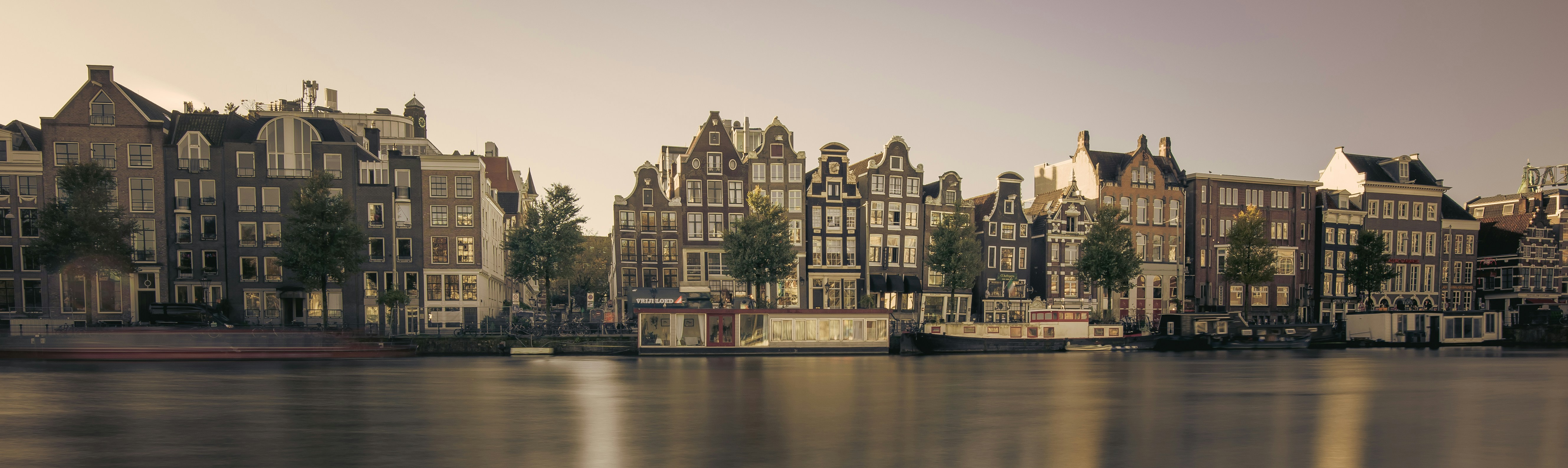 Historic Amsterdam houses with distinct architecture reflected on serene canal waters at dusk.