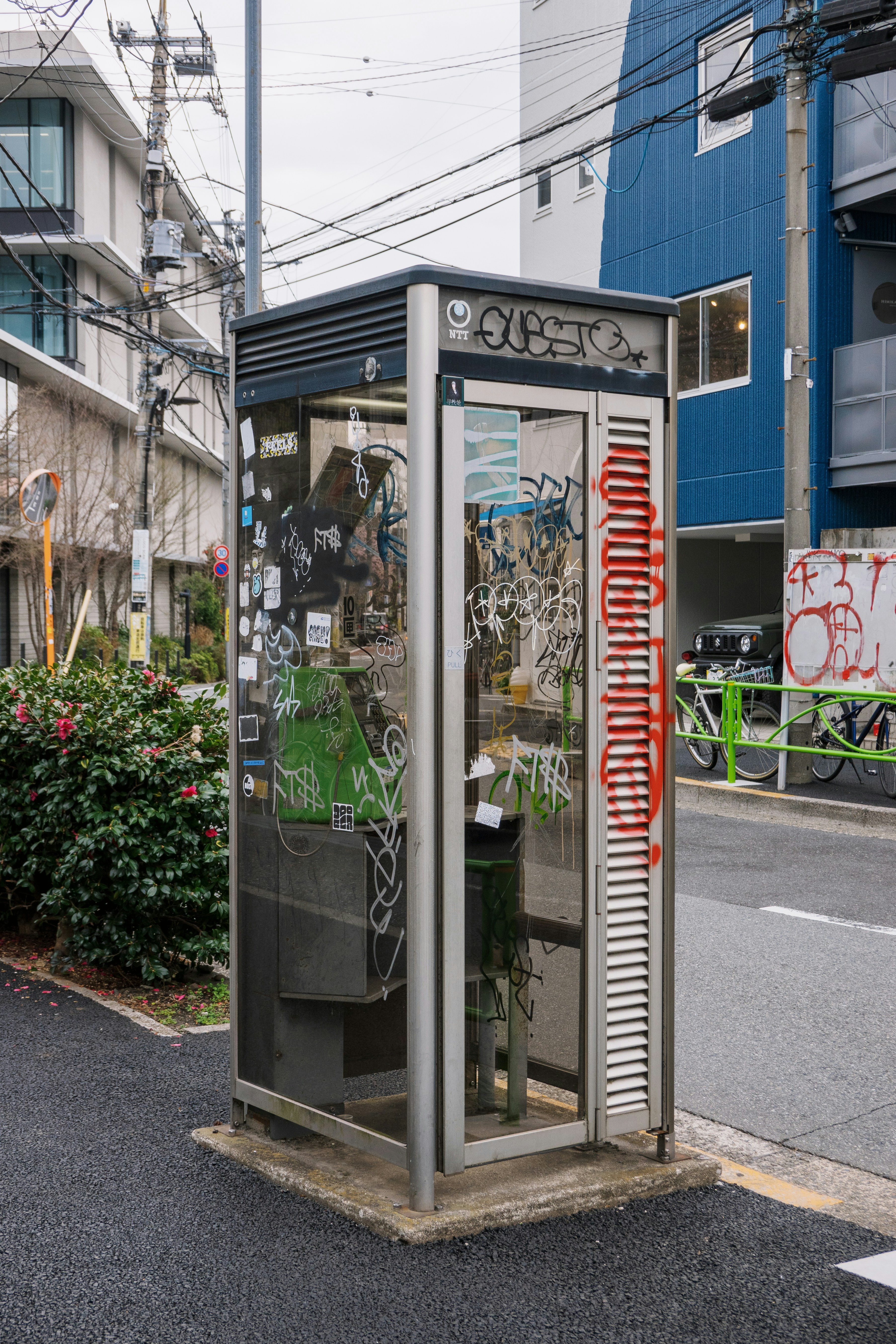 Graffiti-Laced Glass Booth Anchors a Quiet Urban Corner
