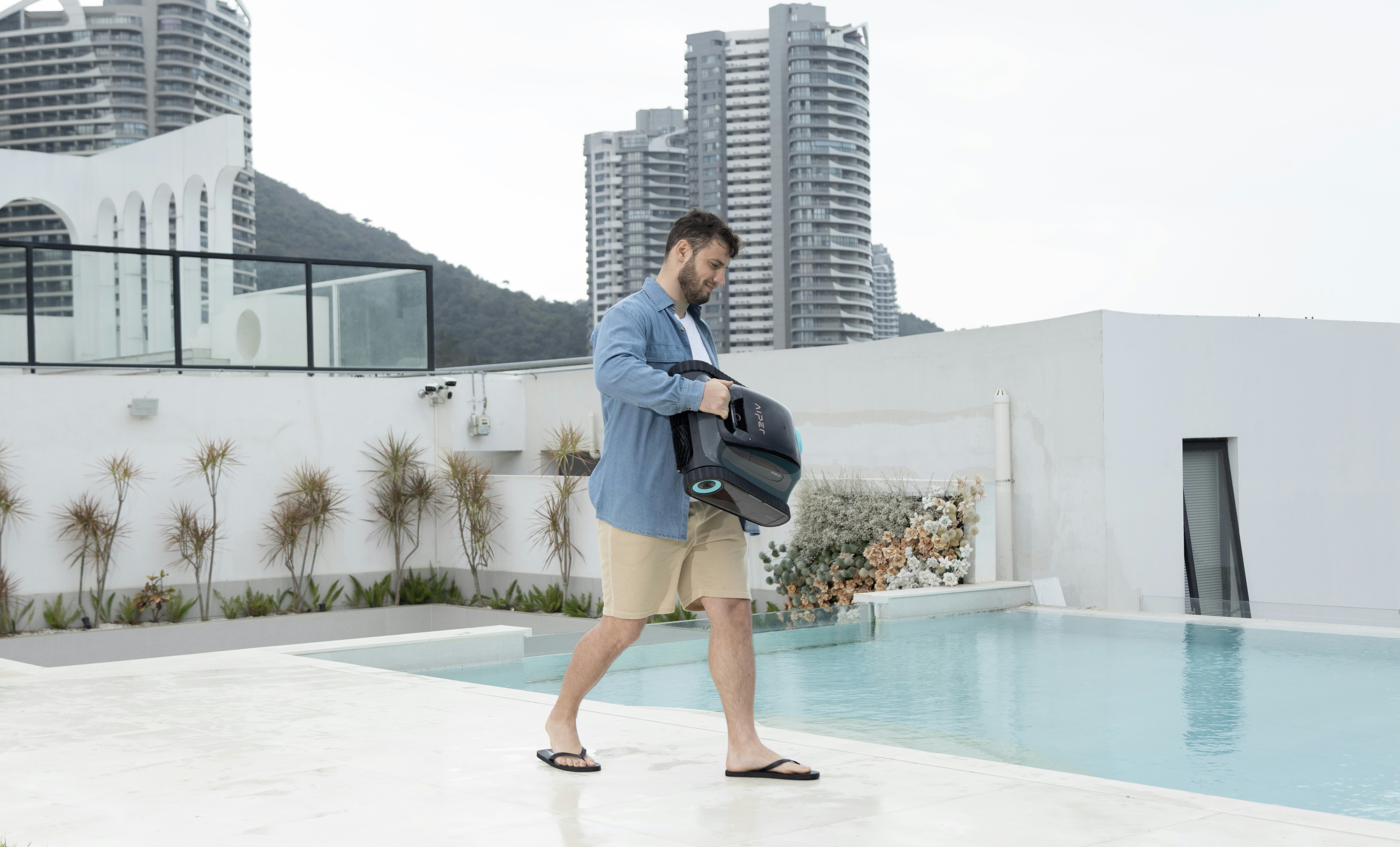 Person preparing to use a pool cleaner next to a sleek, urban swimming pool with a cityscape background.