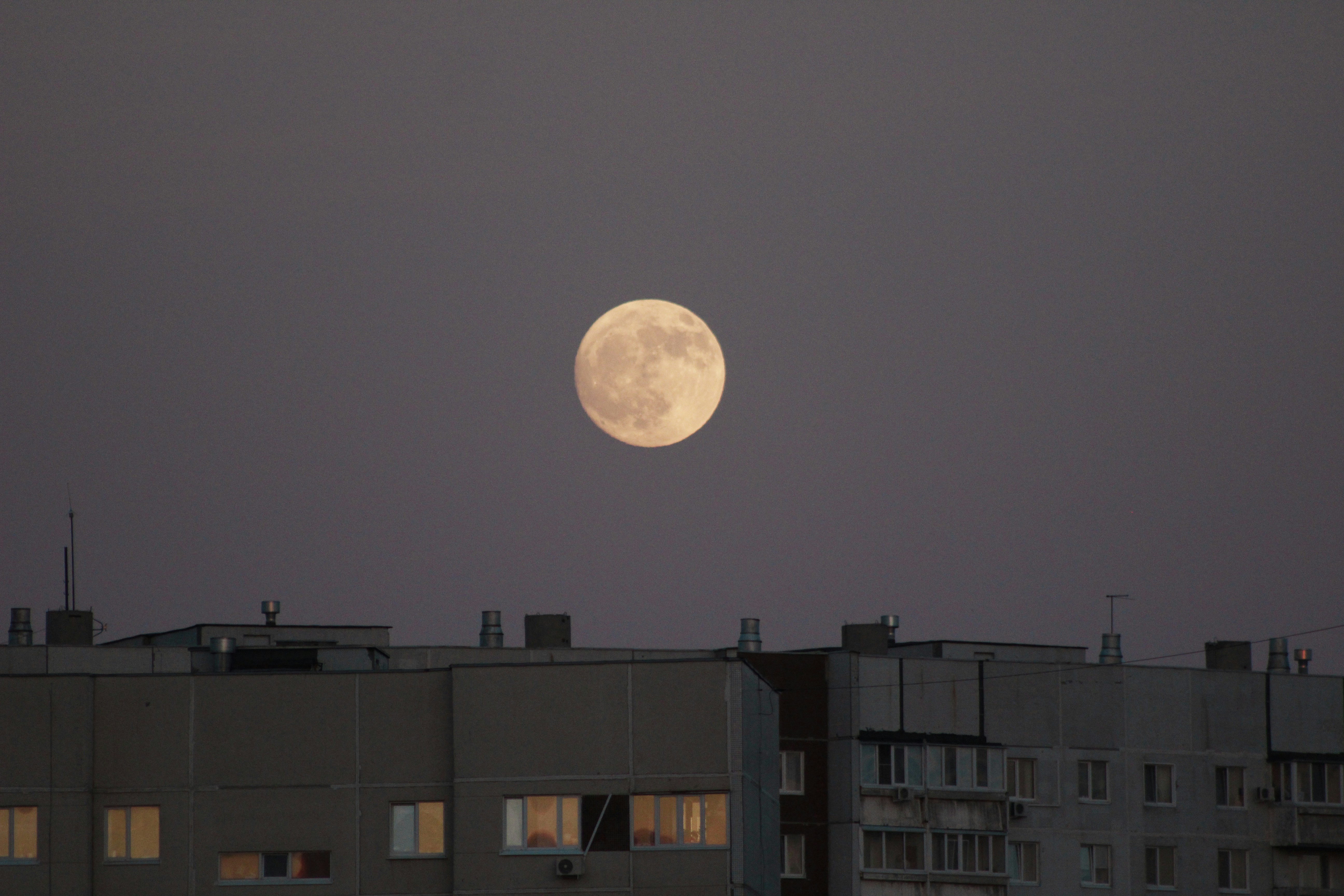 Full moon rising above a city skyline at dusk.