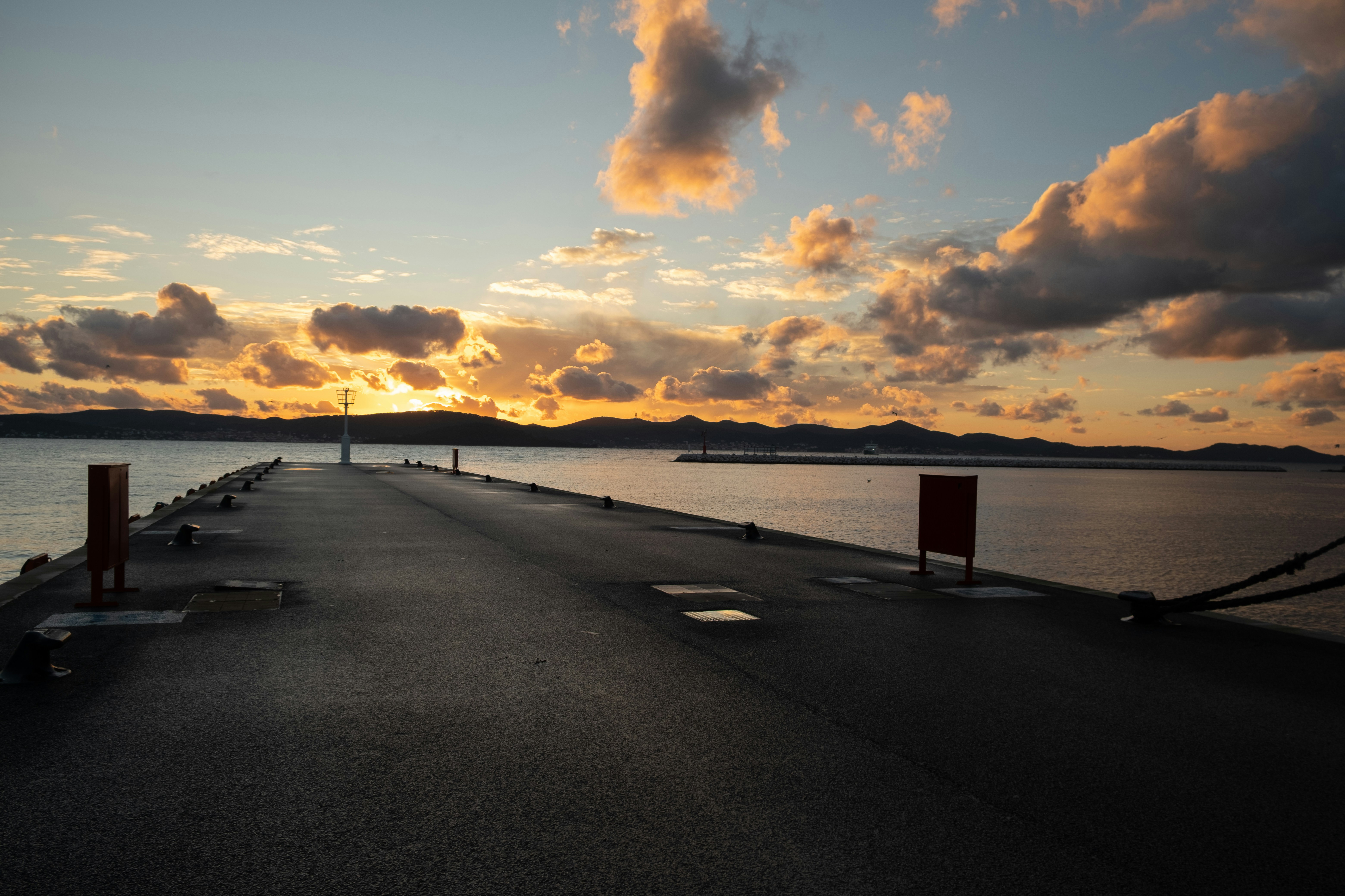 Pier extending into calm waters under a dramatic sunset sky.