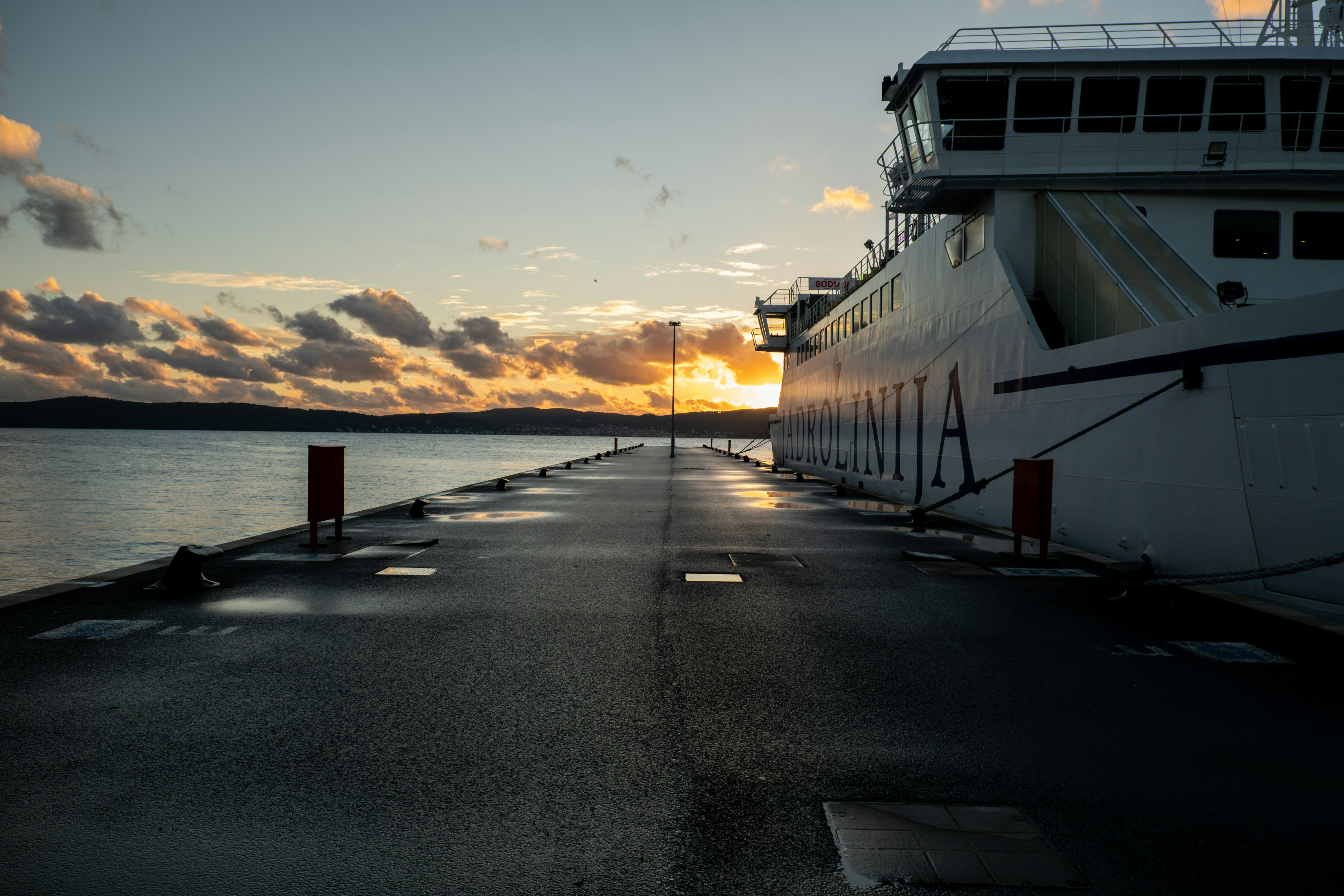 Ferry docked at a pier during sunset, with dramatic clouds and warm hues in the sky.