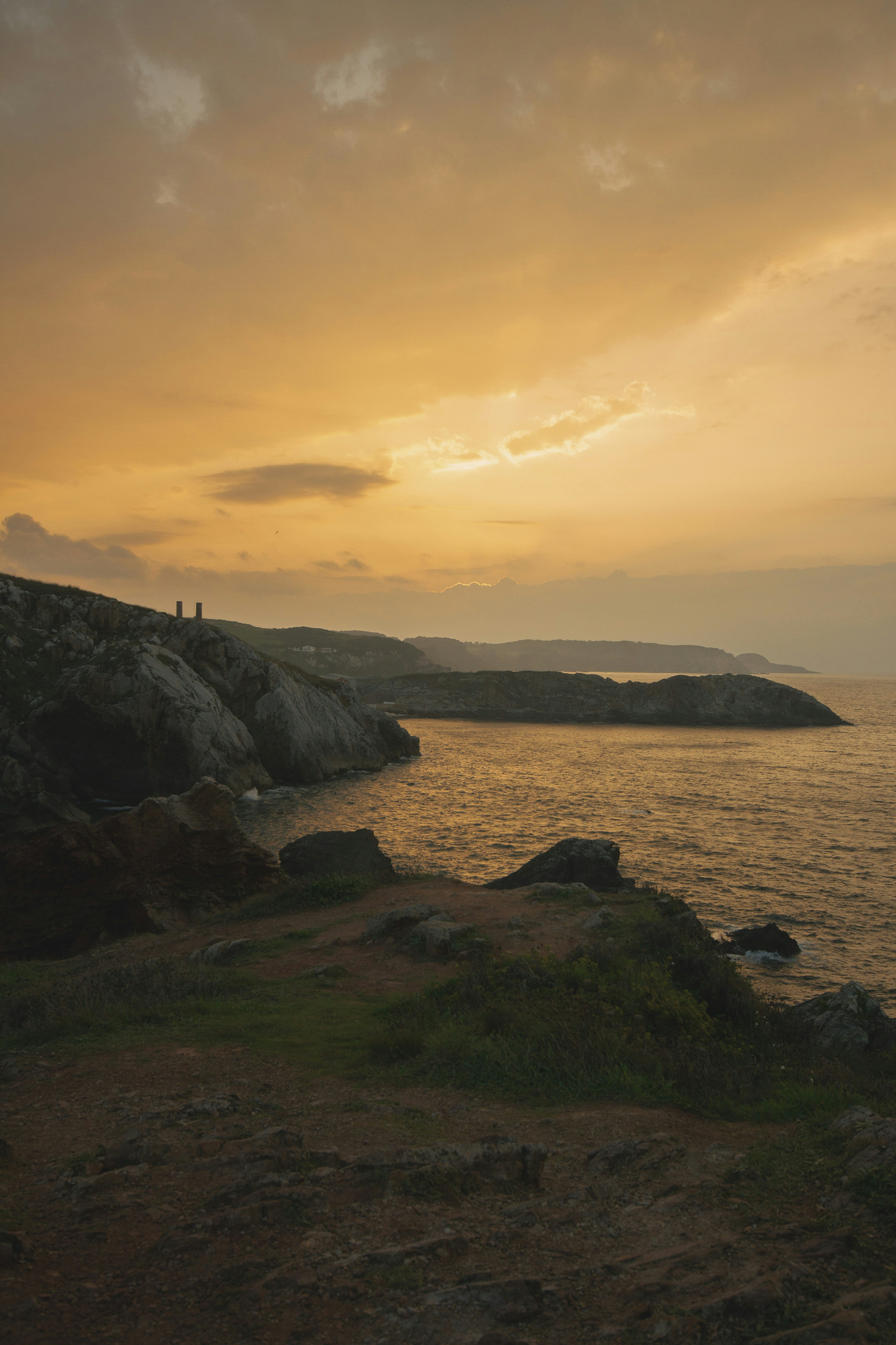 Dramatic coastal landscape with a golden sunset sky casting warm light over rocky cliffs and calm waters.